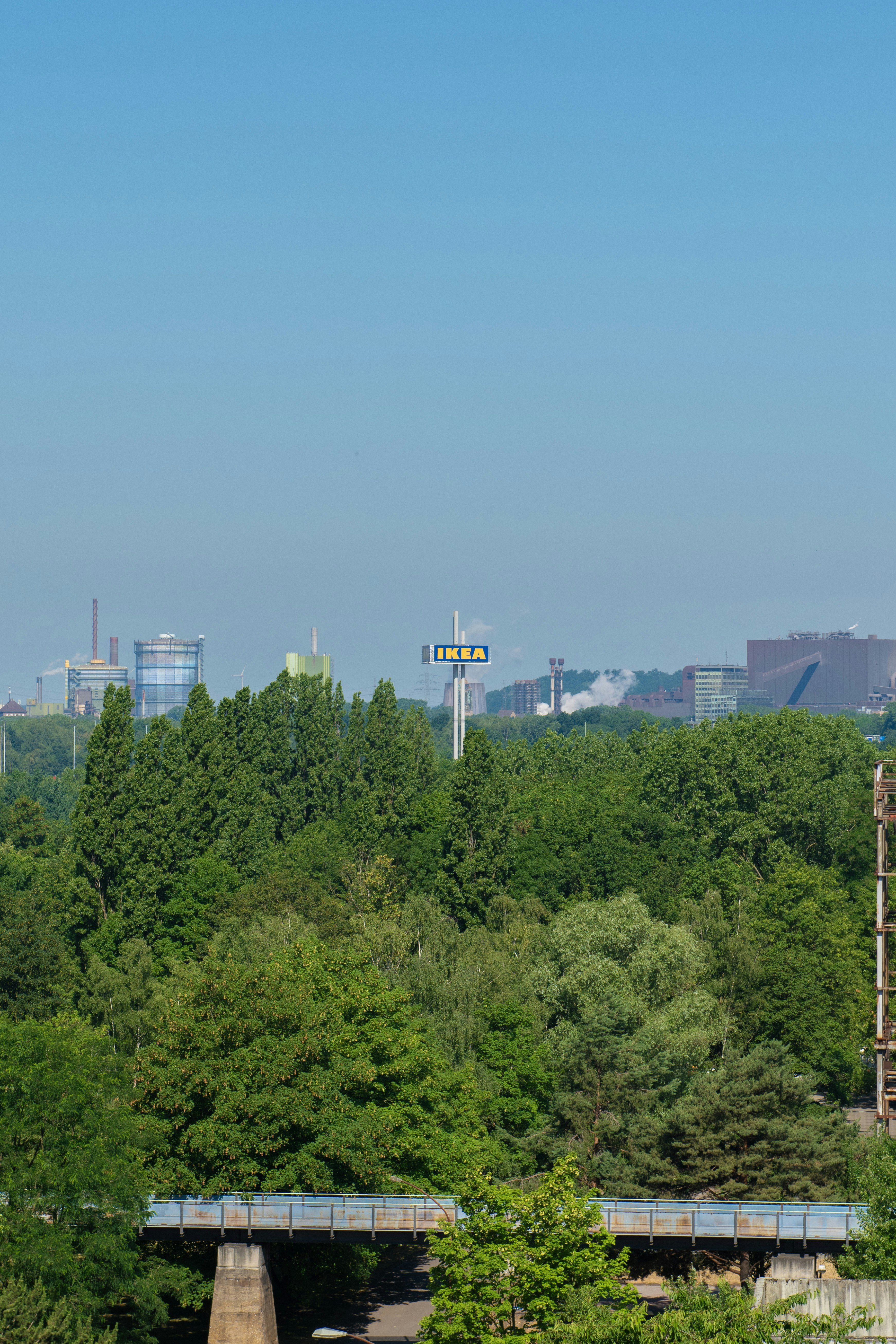 Trees with an Ikea billboard/sign in the distance, industry stuff and a clear blue sky.