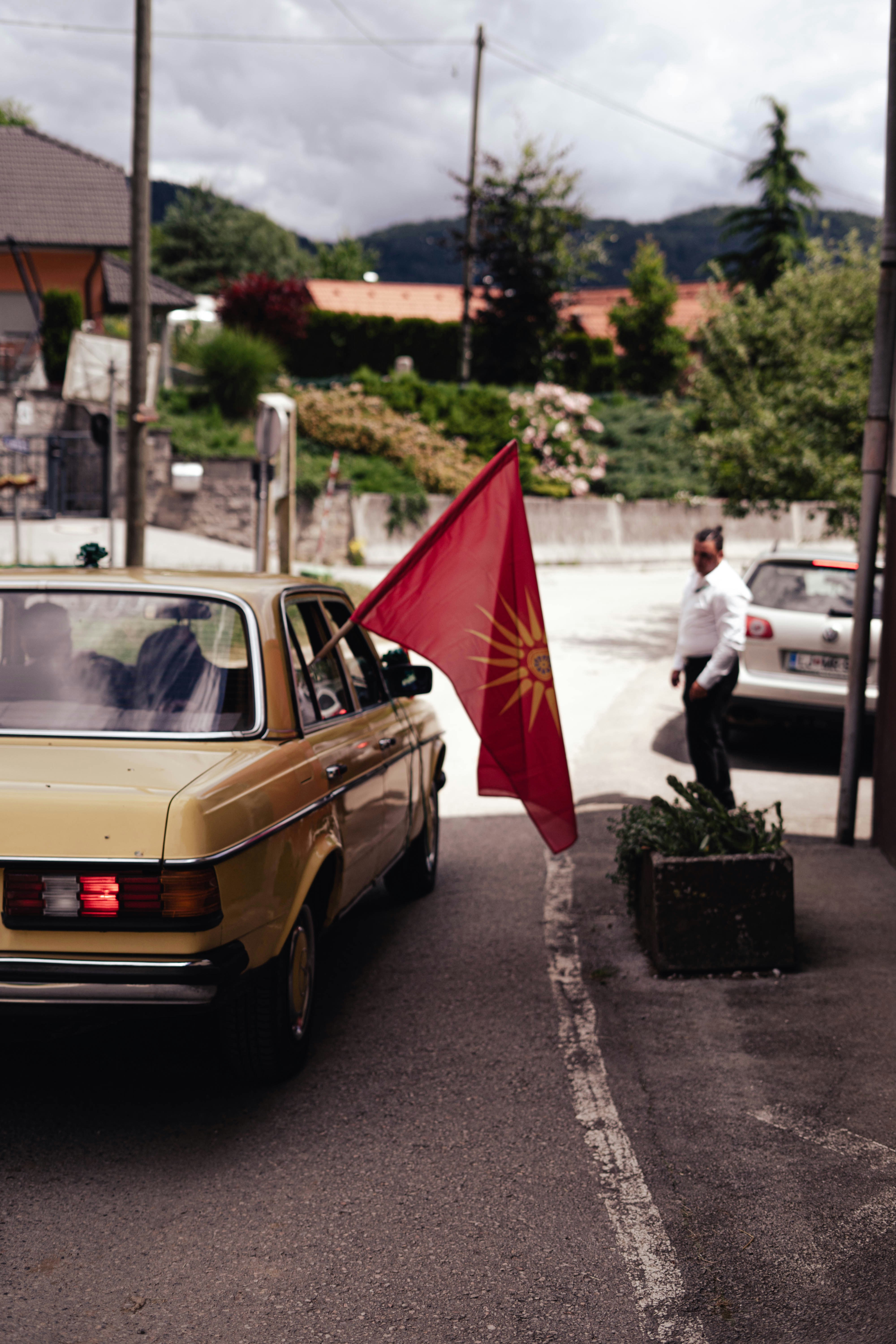 Sunburst Flag by the Curb: A Vintage Sedan Anchors a Quiet Street Scene
