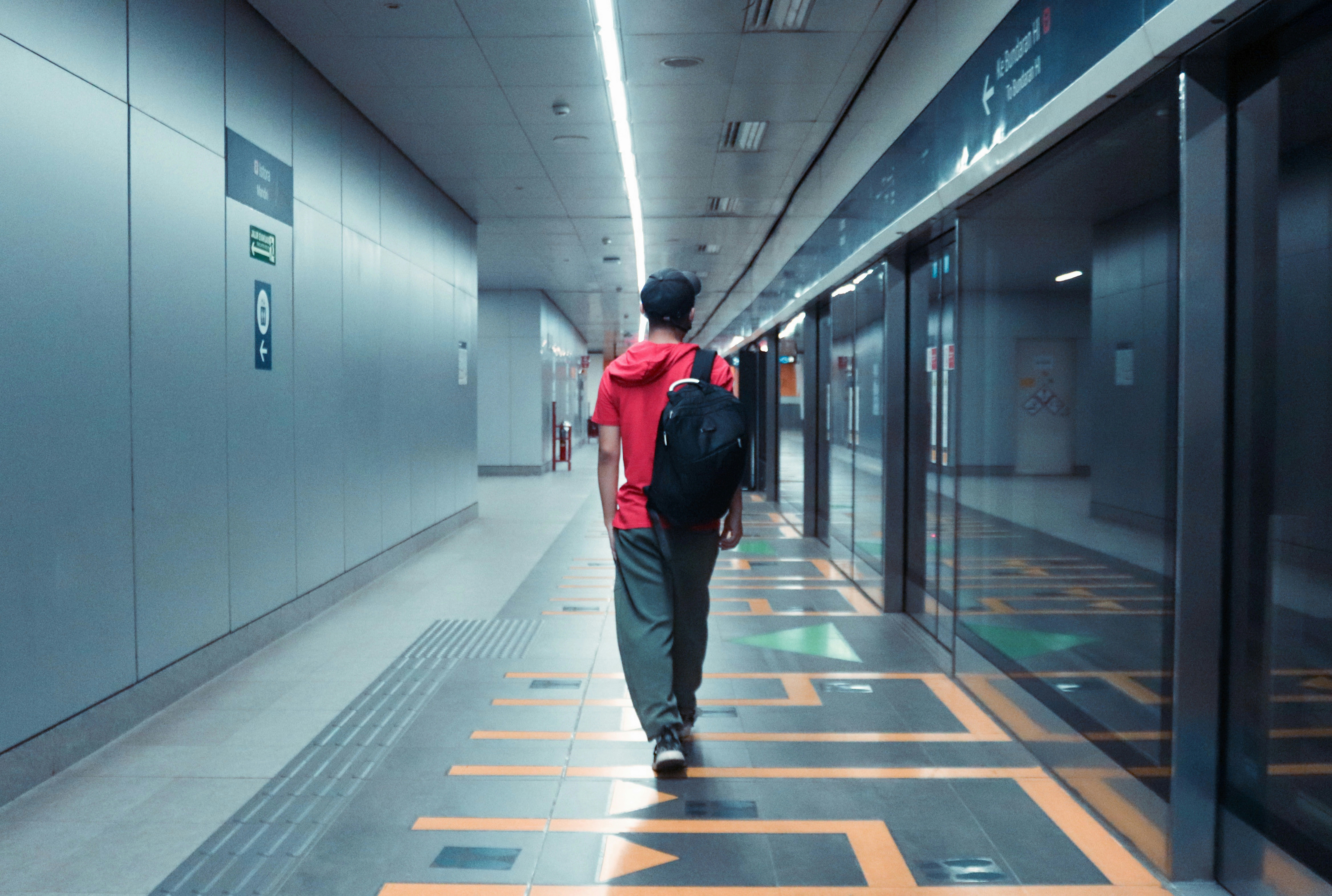 A lone figure walks through a modern subway corridor, surrounded by sleek walls and illuminated pathways.
