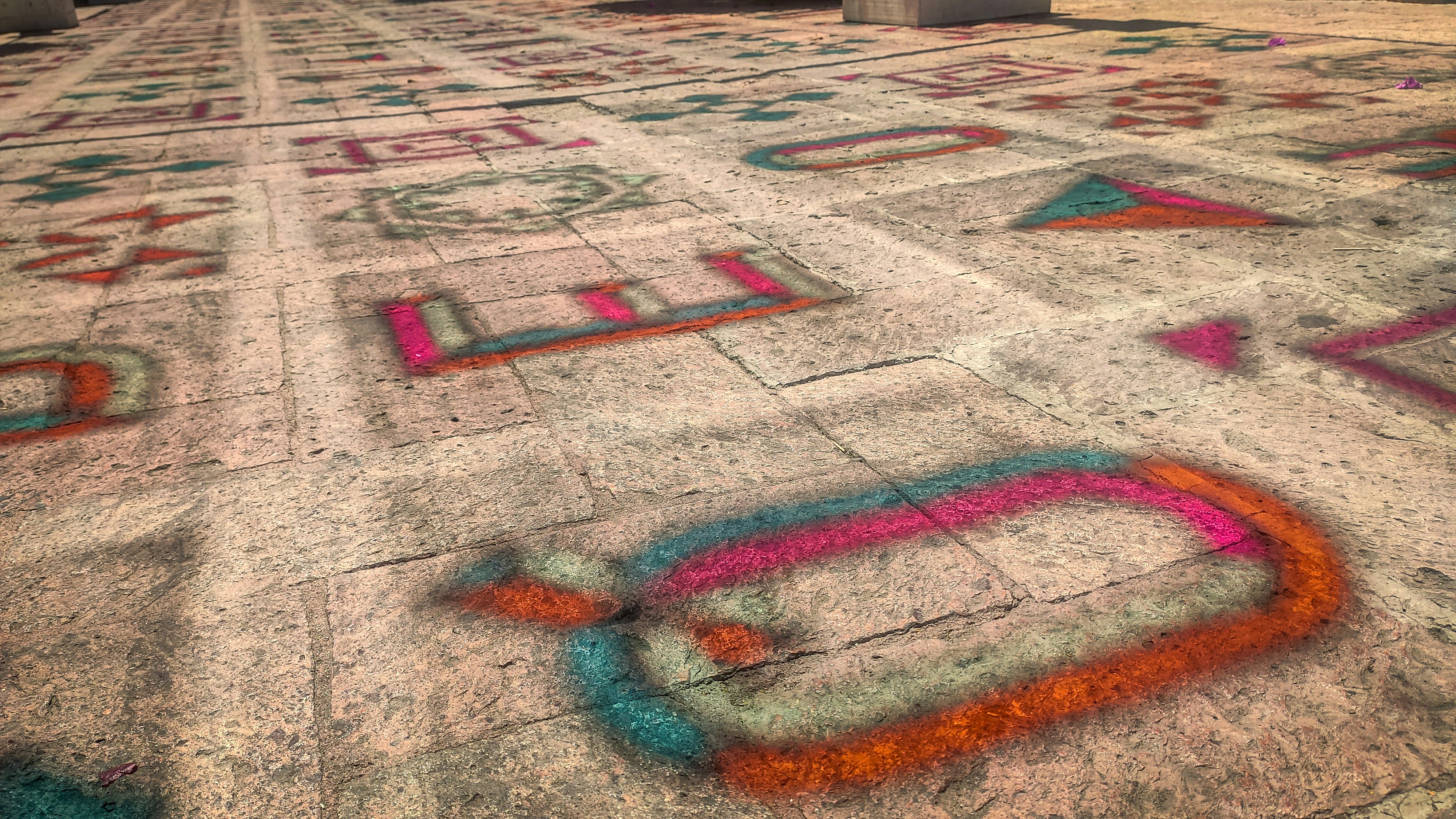 Colorful chalk graffiti on a weathered tile floor forms a neon loop and scattered geometric shapes.