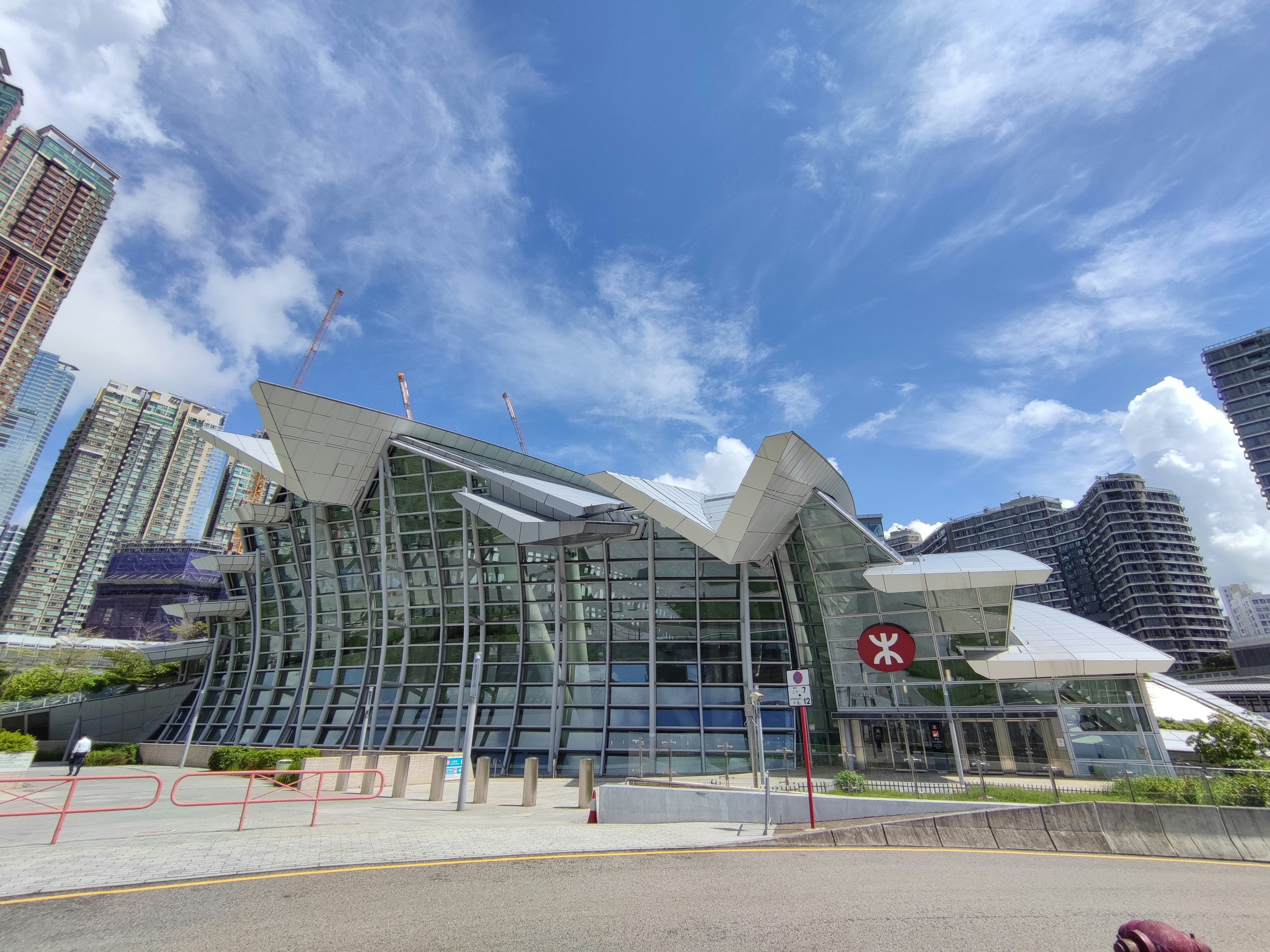 Angular glass atrium sits against a bright blue sky, framed by surrounding skyscrapers and a pedestrian plaza.