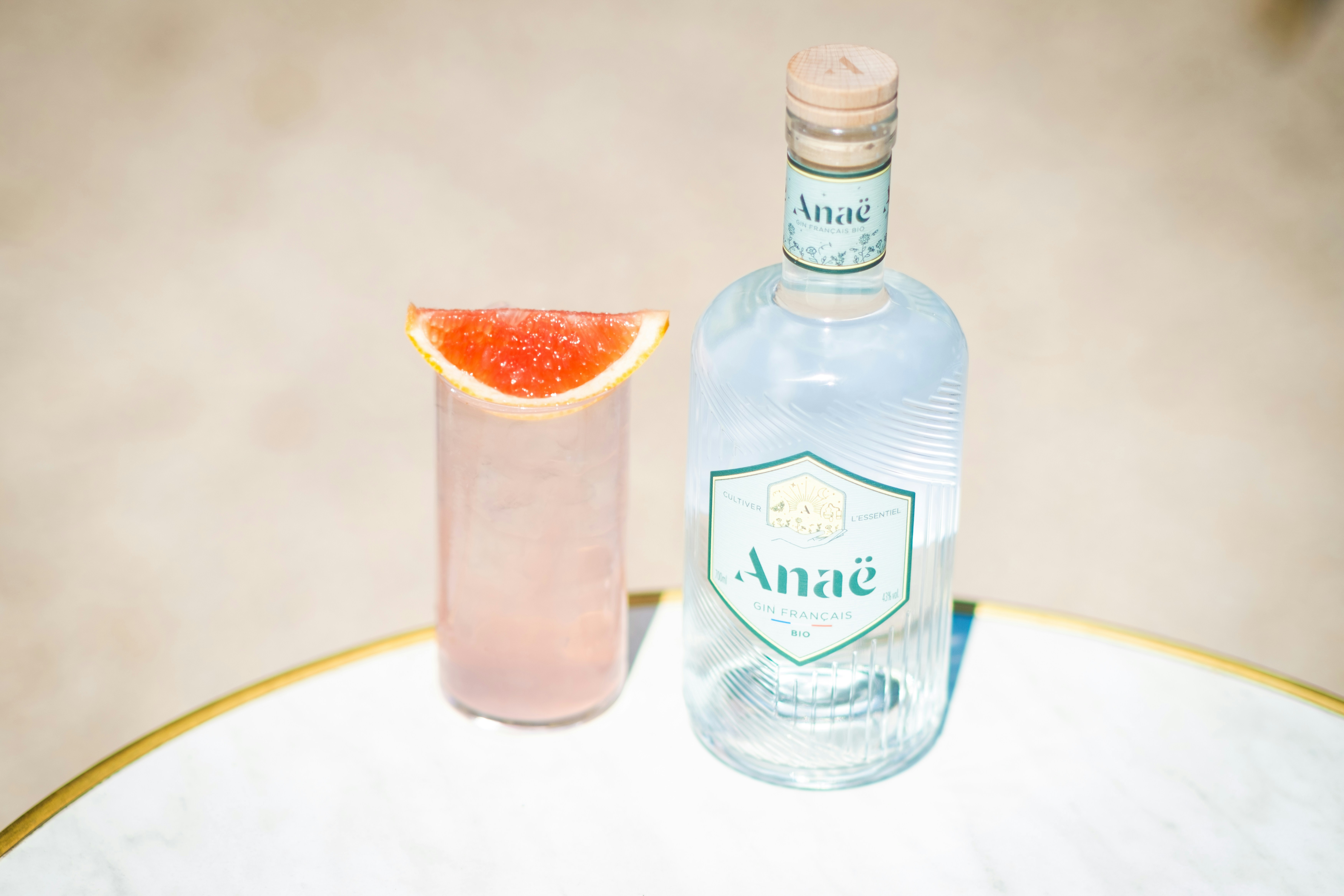 Sunlit Duo: A Blush Cocktail and a Crystal Gin Bottle on a Glossy Table