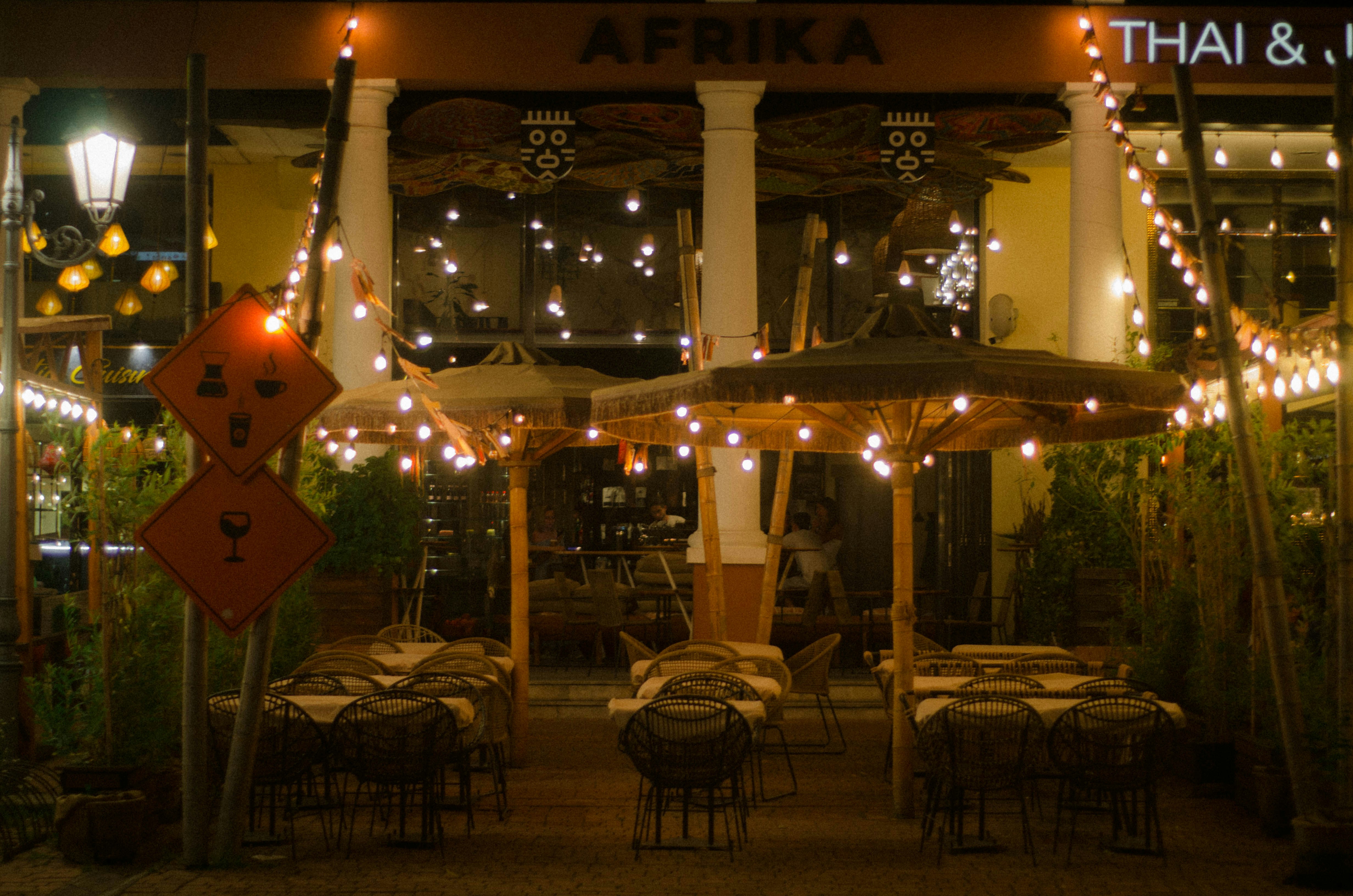 Cozy outdoor dining area at Afrika restaurant adorned with warm string lights and decorative umbrellas. The inviting atmosphere beckons patrons to enjoy a night out.