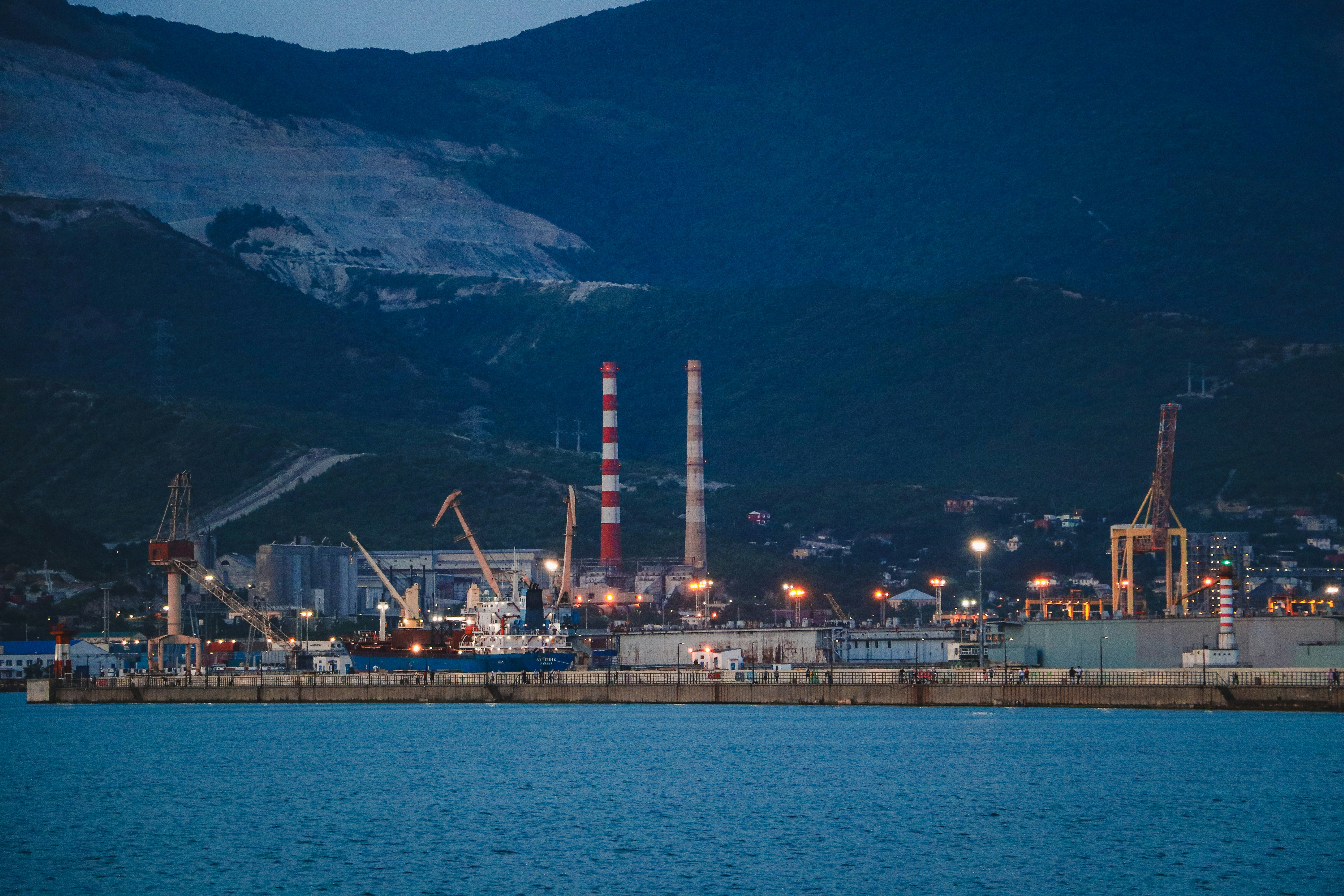 Industrial waterfront under evening haze with smoke stacks against mountains