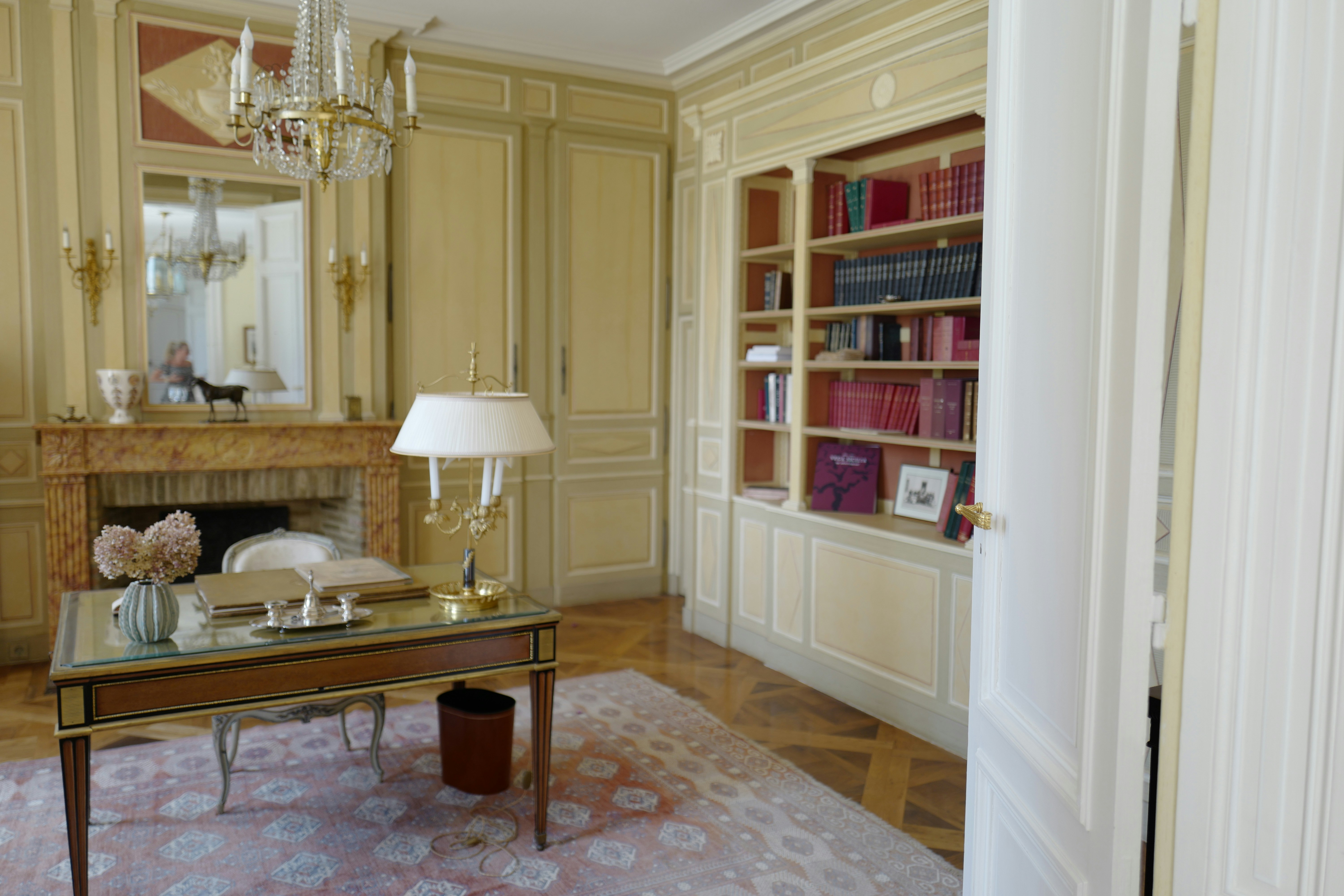 Stylish interior featuring a wooden table with floral decor, a chandelier, and a well-stocked bookshelf, all set in a softly lit room.