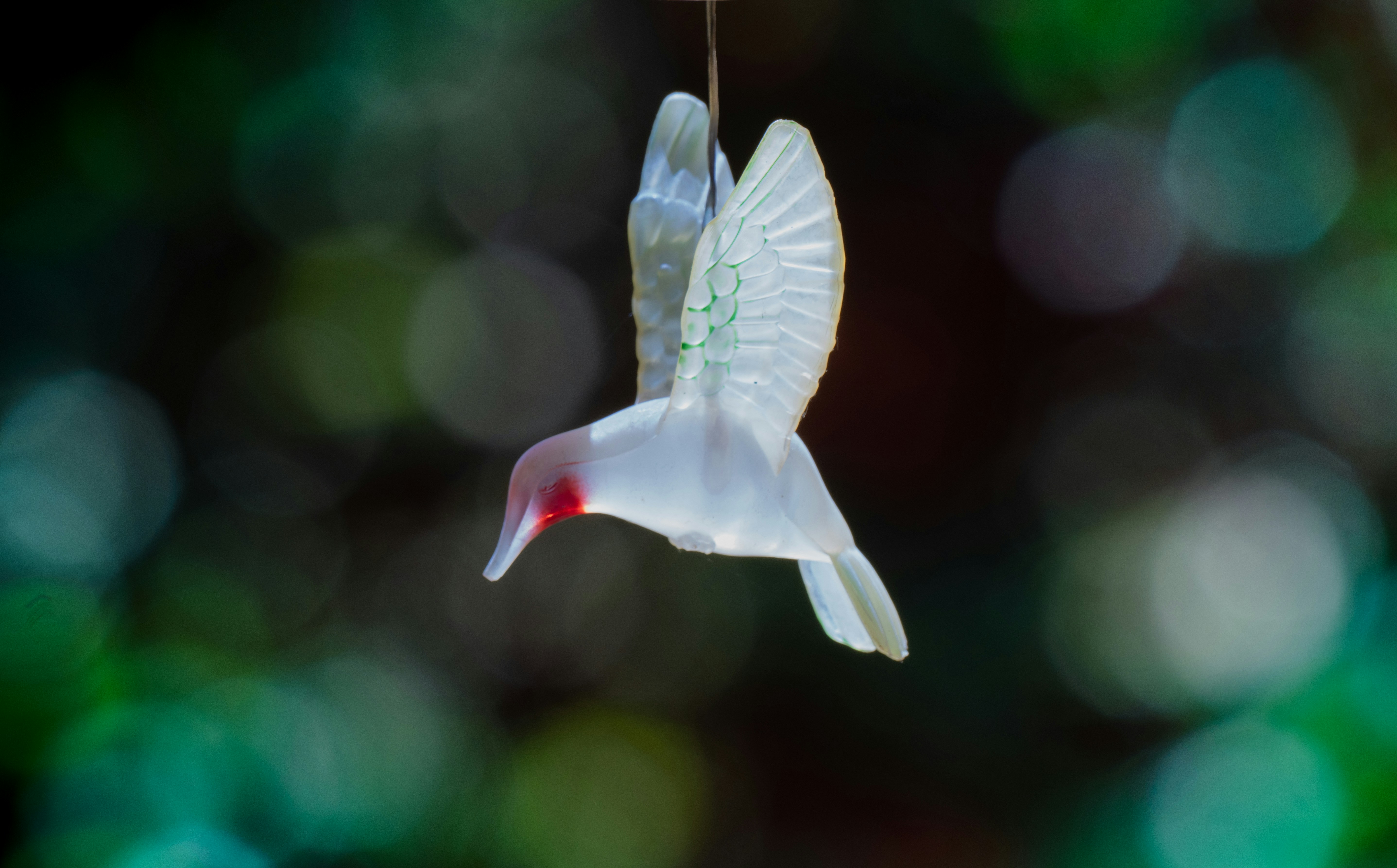Suspended White Hummingbird Ornament Amid Emerald Bokeh