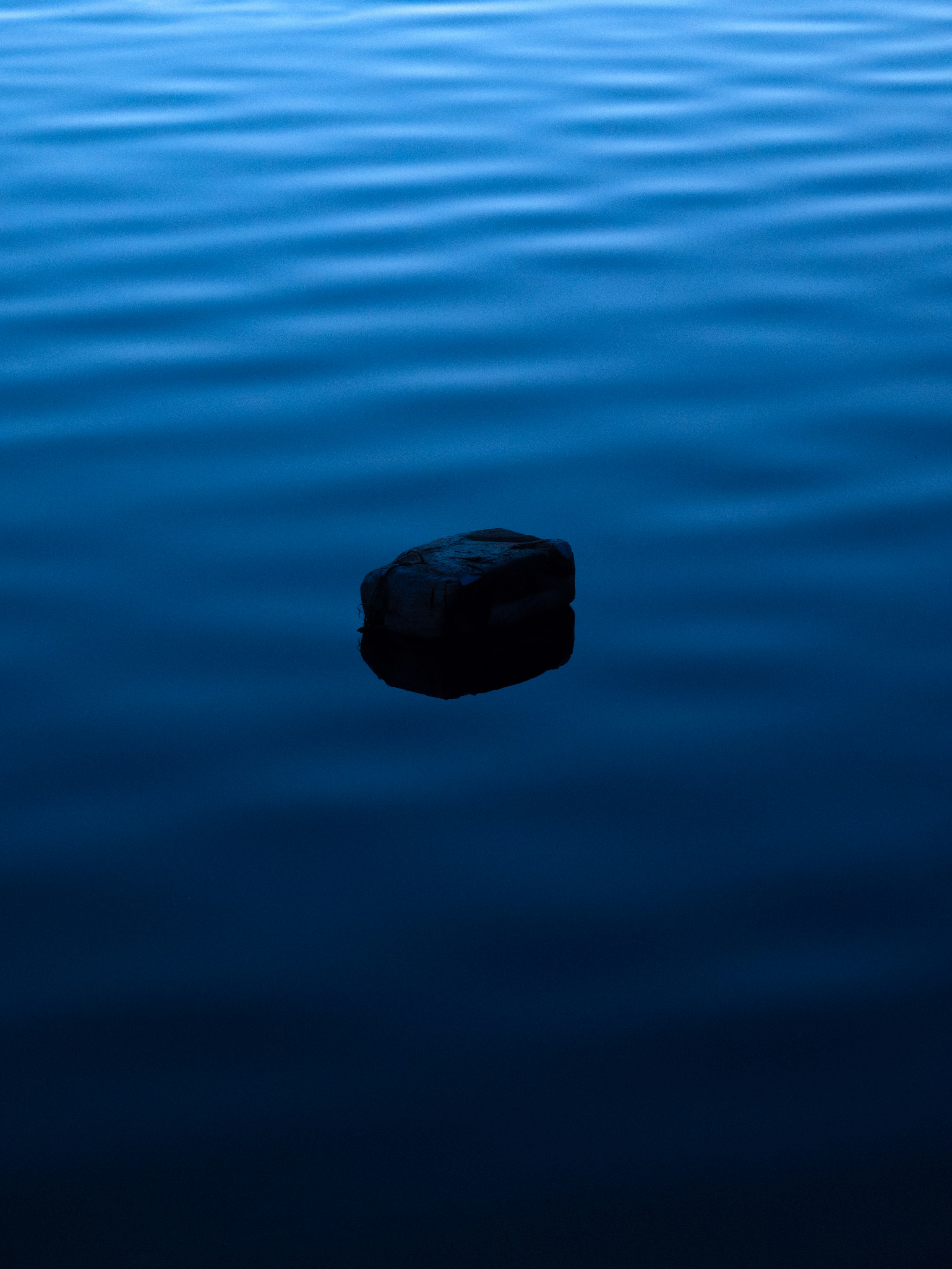 Floating Monolith: A lone rock drifting in midnight blue water