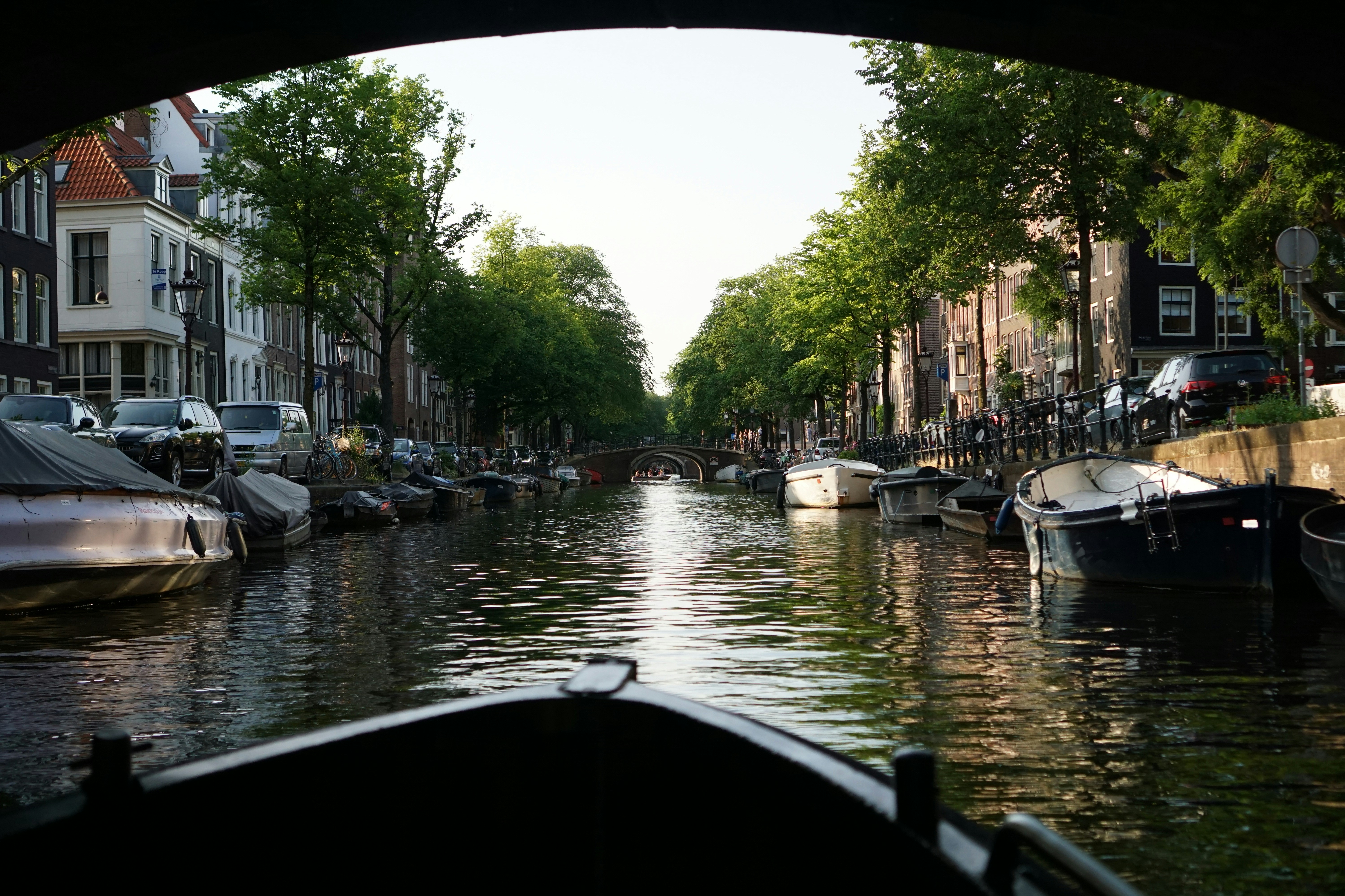 Toward the Arched Bridge: Sunlit Canal from a Boat