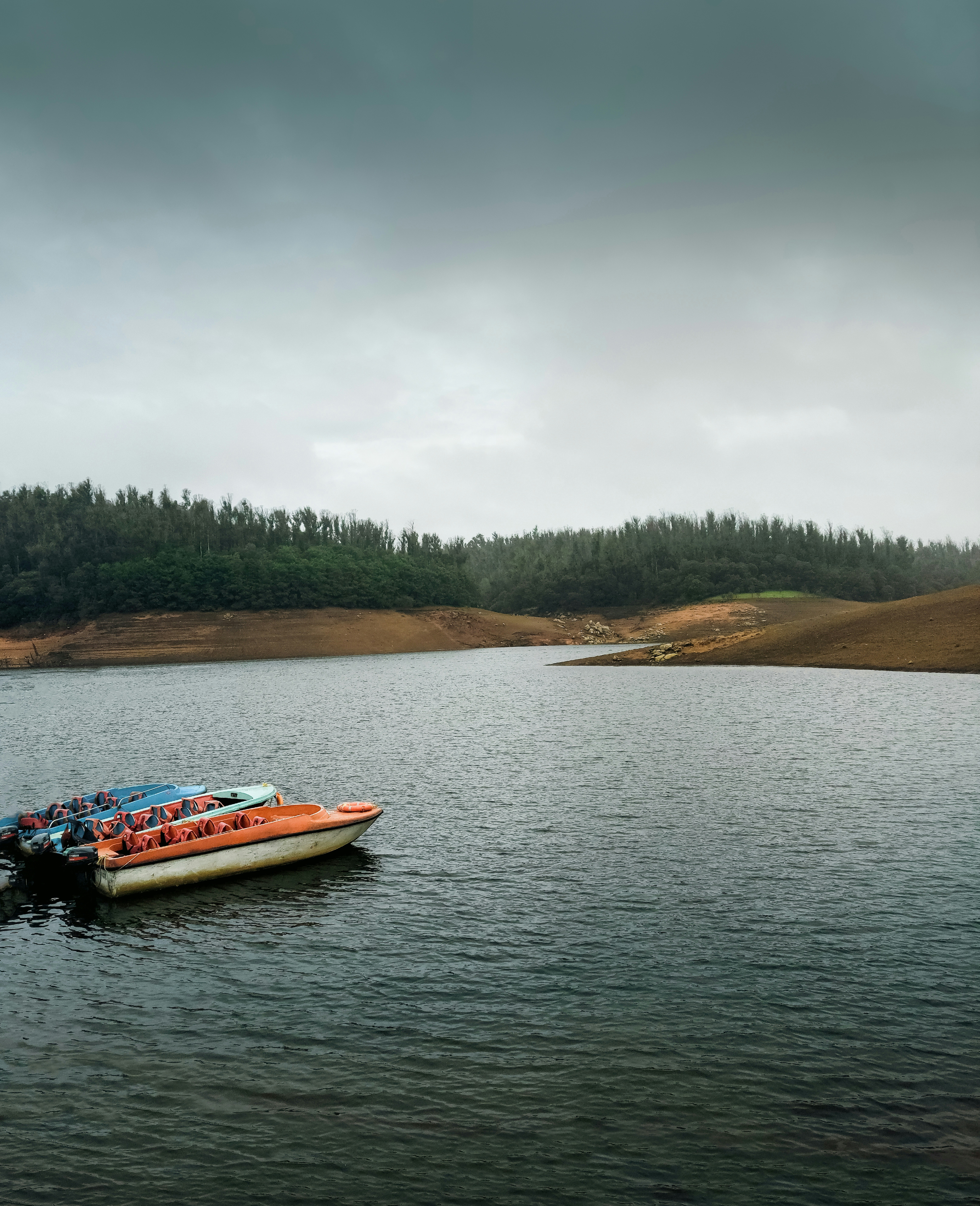 Colorful boats docked on a calm lake with forested hills and a moody, cloudy sky.