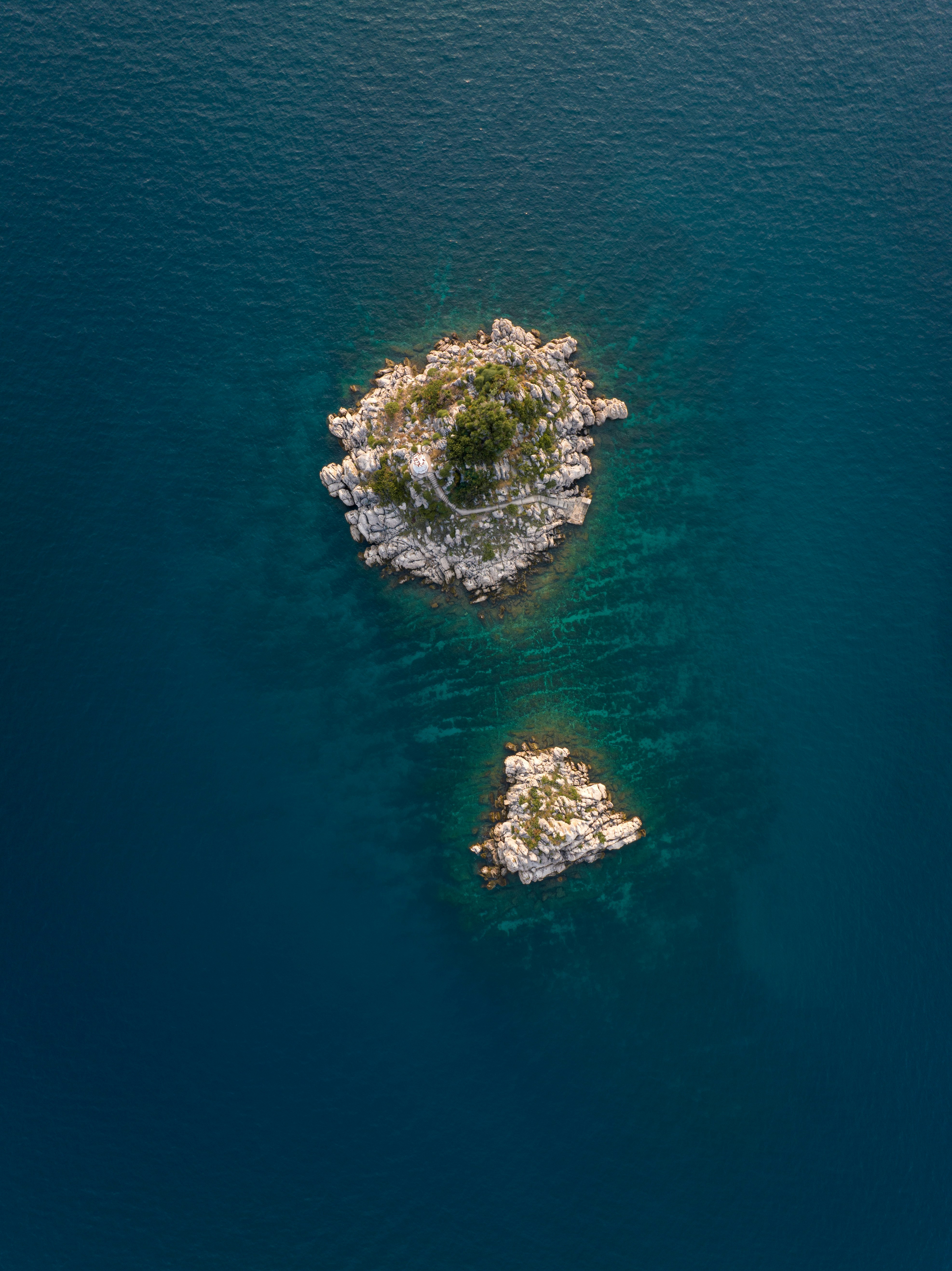 Two small islands surrounded by deep blue waters, featuring rocky shores and lush greenery on the larger island.
