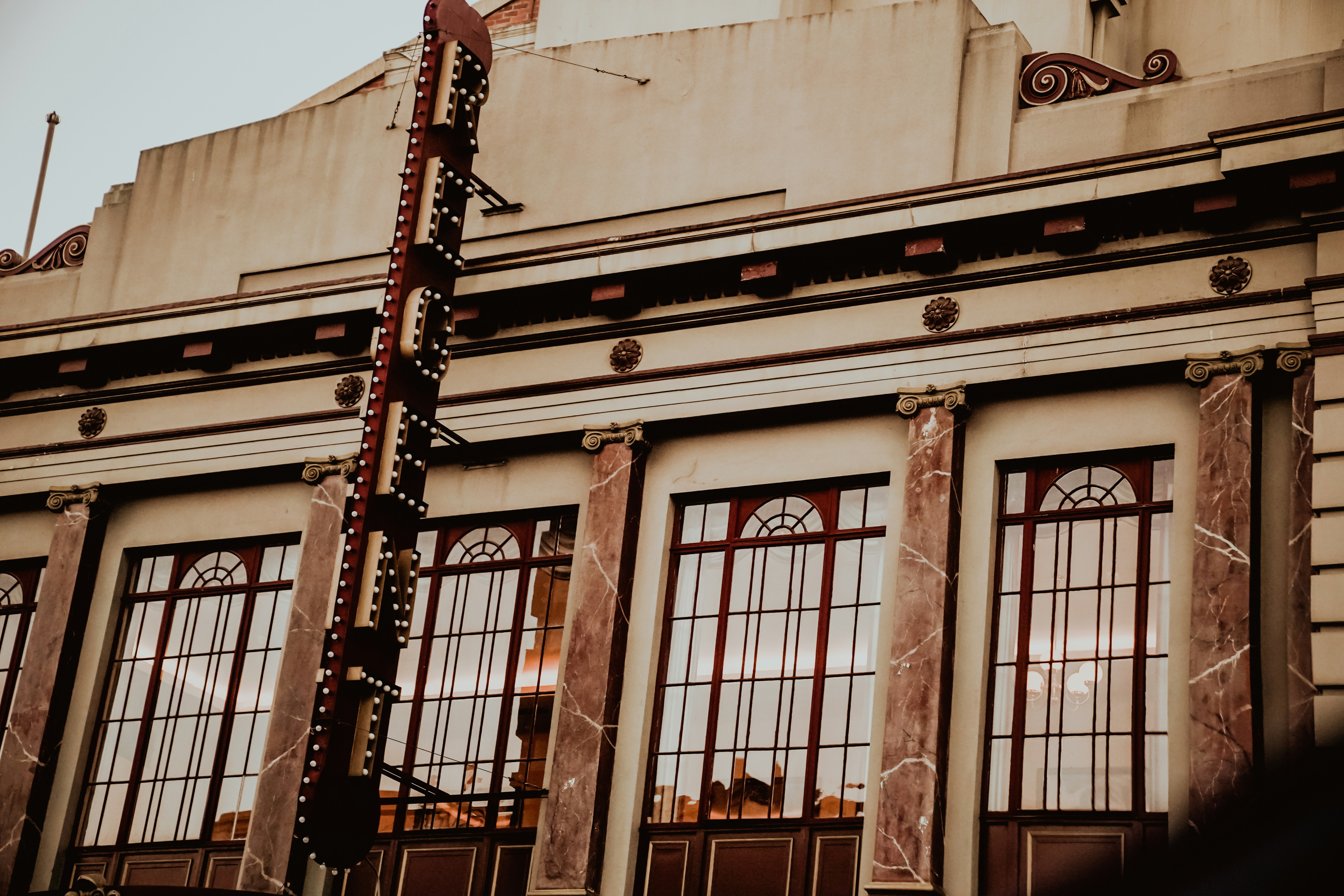 Historic building with large windows and a vertical theater sign against an overcast sky.