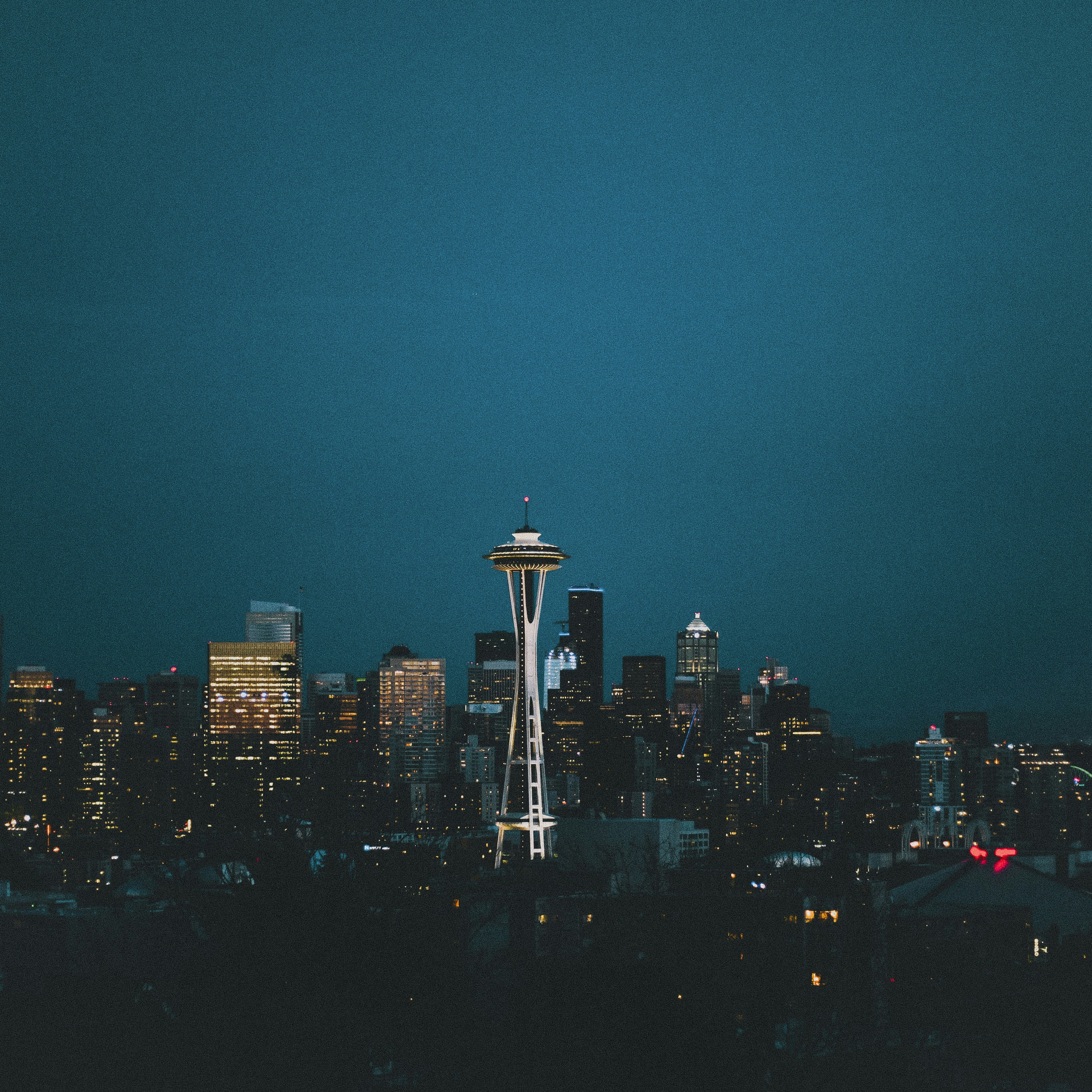 Seattle's iconic Space Needle towers over a shimmering cityscape at twilight, illuminated against a deep blue sky.
