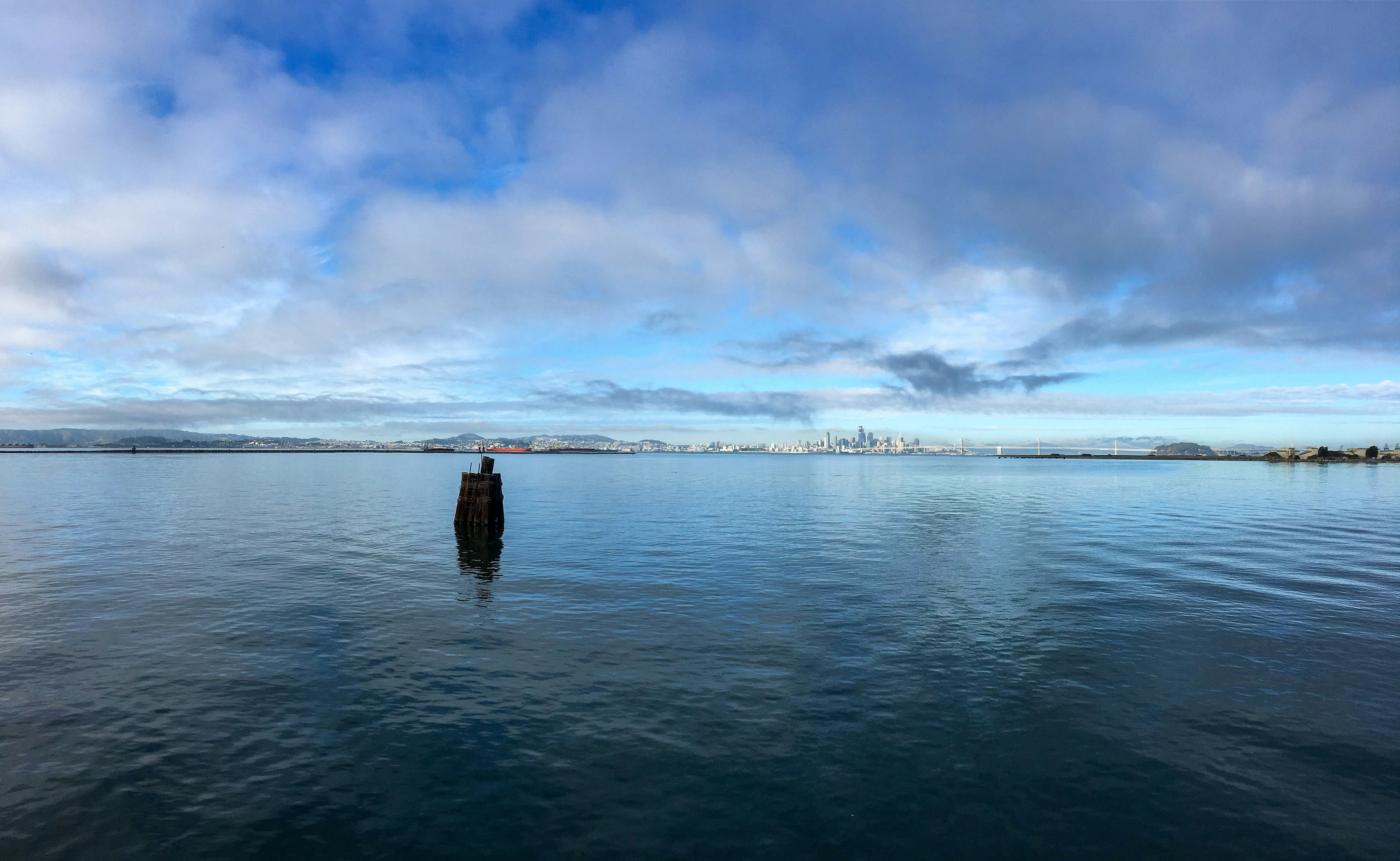 Solitary wooden post standing in calm blue water under a cloud-filled sky.
