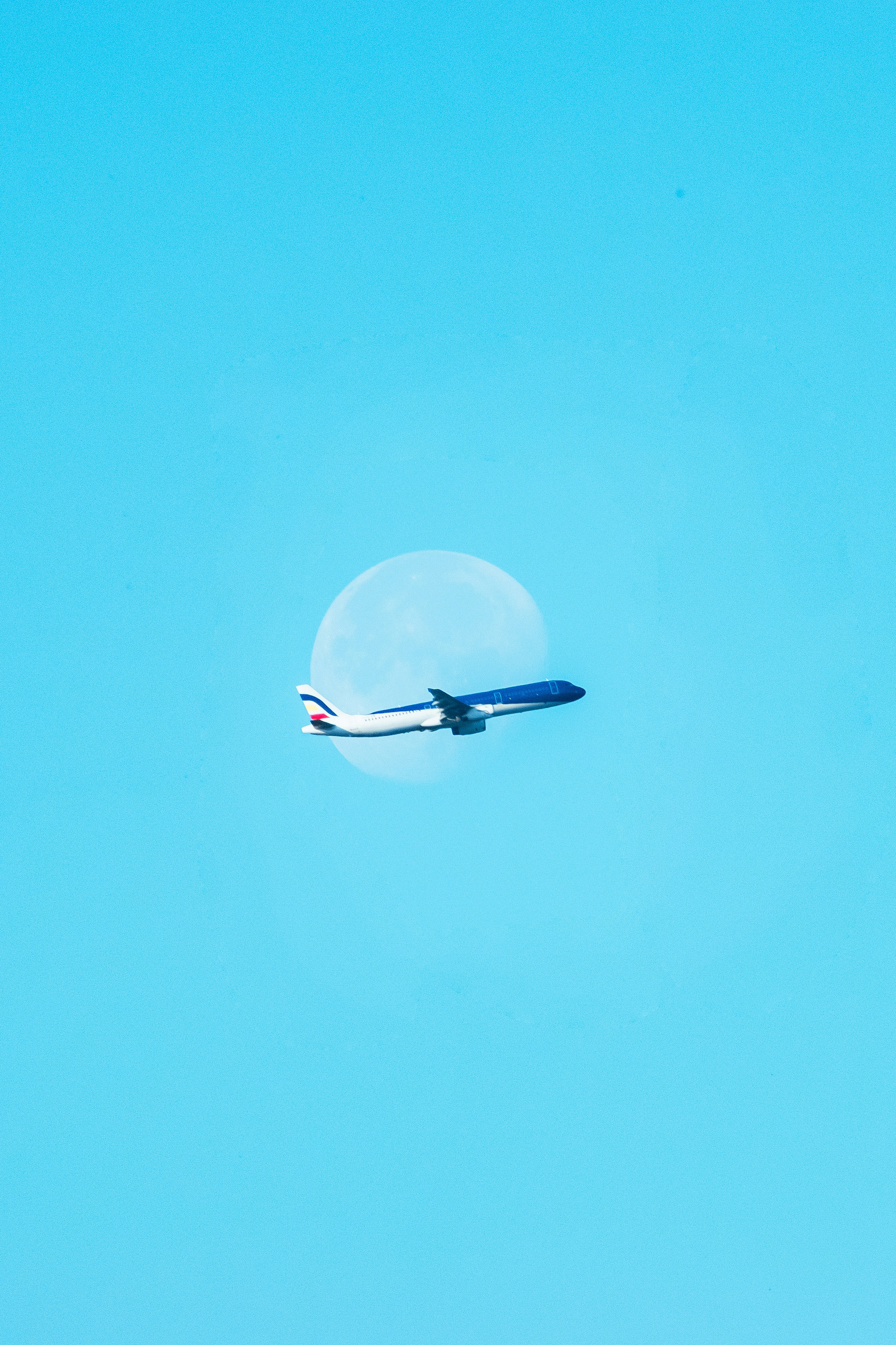Moonlit Passage: A Jet Glides Before a Giant Moon in a Cerulean Sky