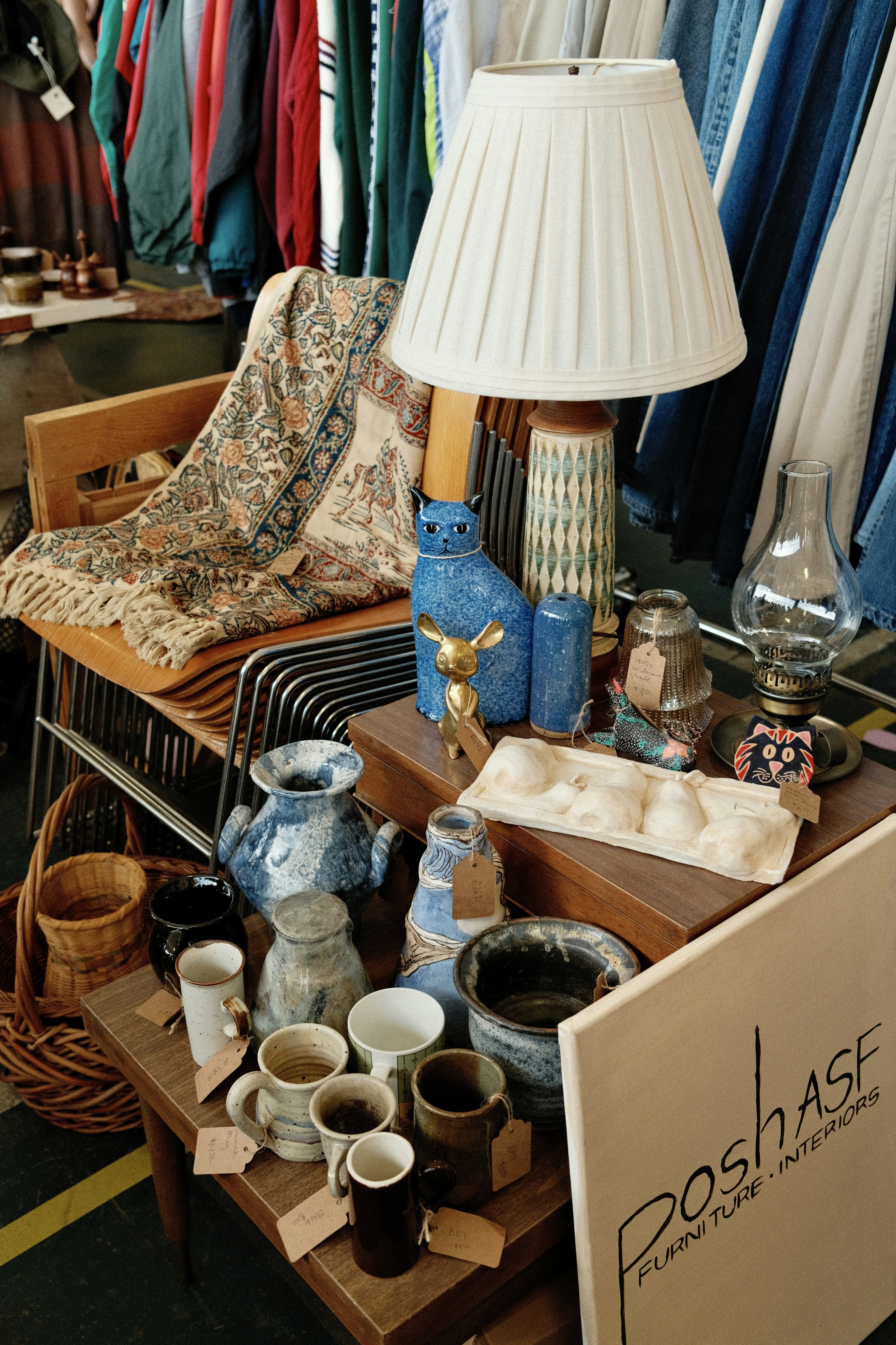 Blue ceramic cat anchors a boutique still life amid textiles, mugs, and a softly lit lamp