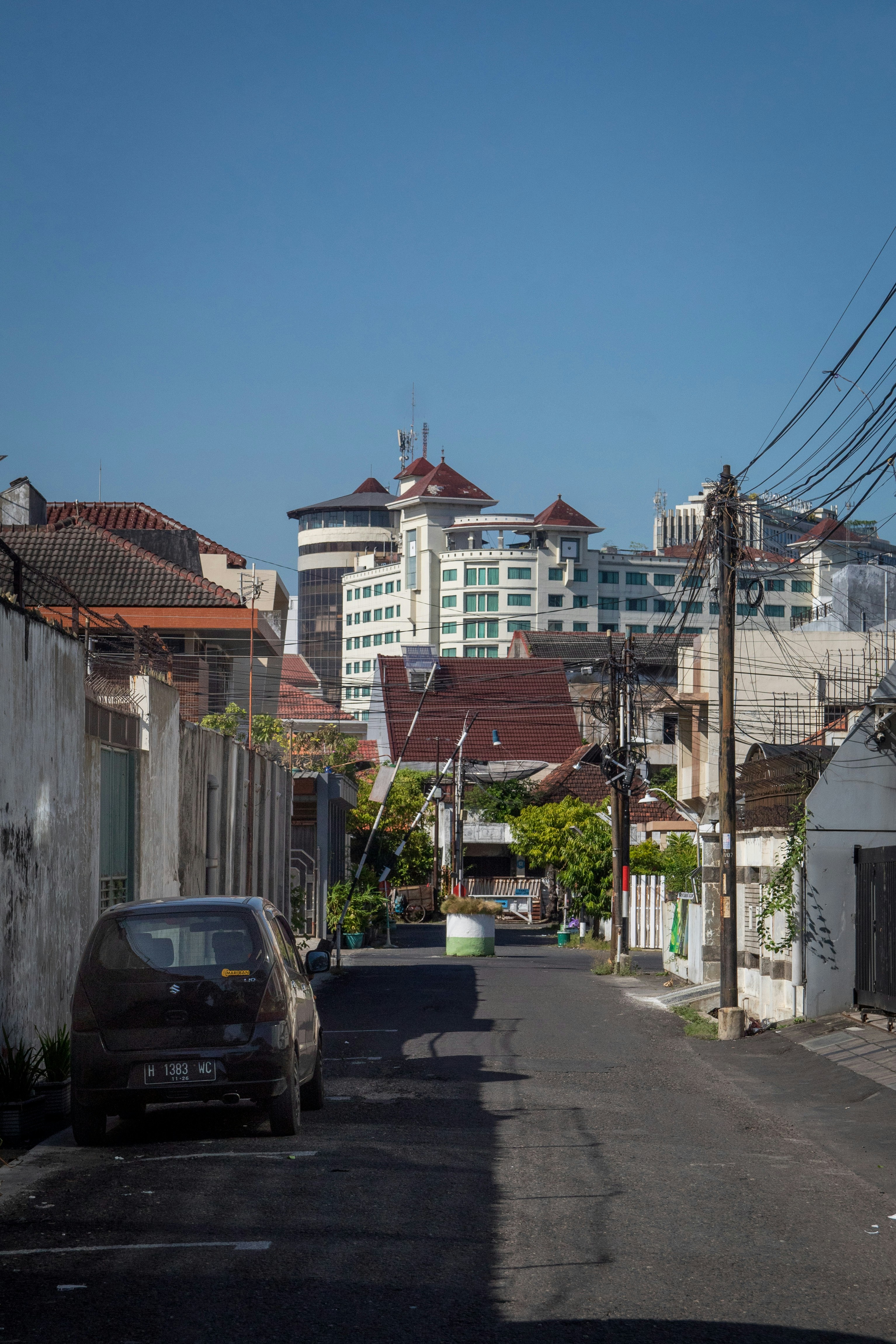 A quiet street scene showcasing a blend of traditional and contemporary architecture, with a parked car and lush greenery lining the road.