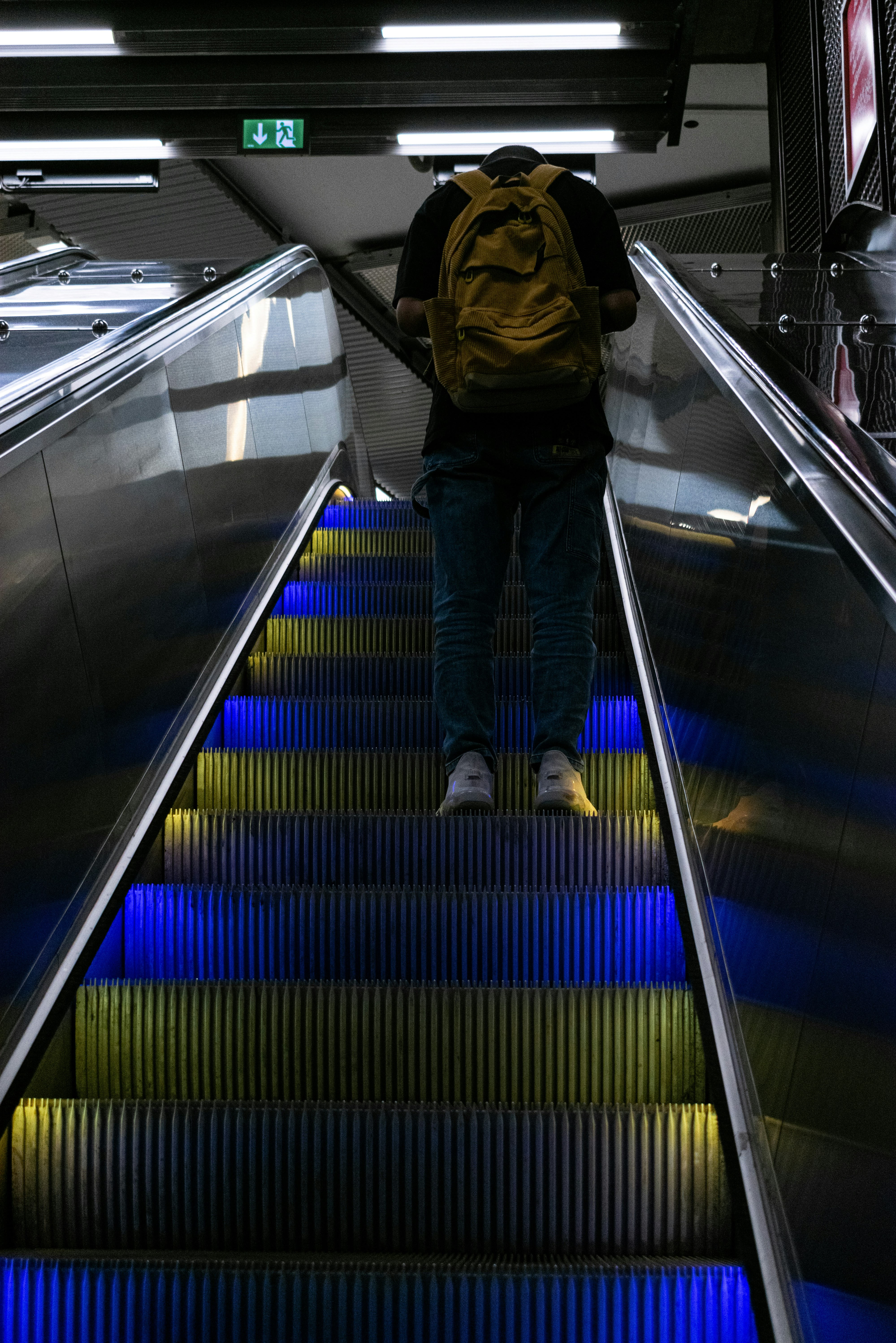  commuter ascending a neon-lit escalator into the metro tunnel