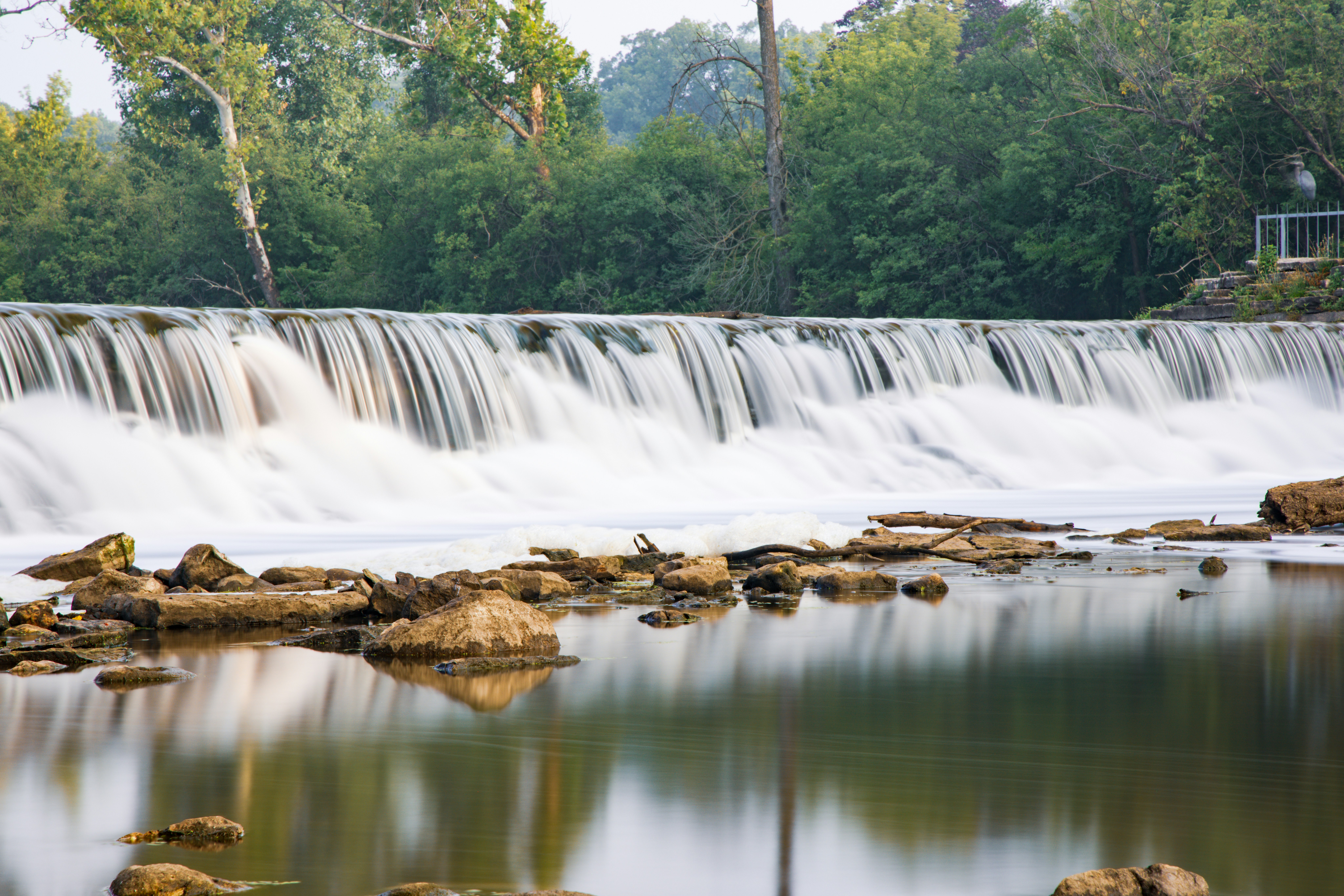 Smooth waterfall cascading over rocks with lush green trees in the background.