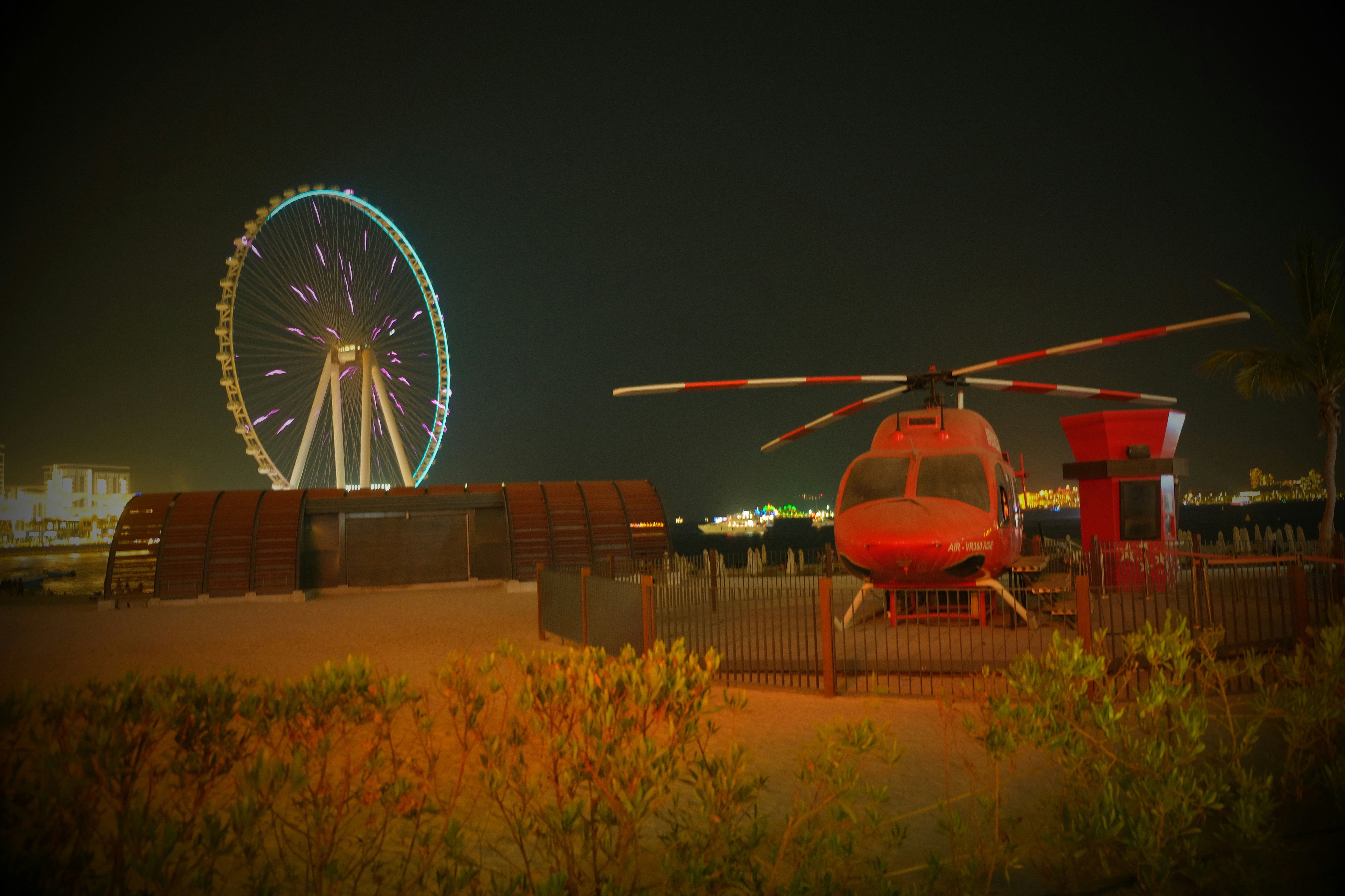 Neon Ferris Wheel at Night: A Red Helicopter Guards the Quiet Promenade