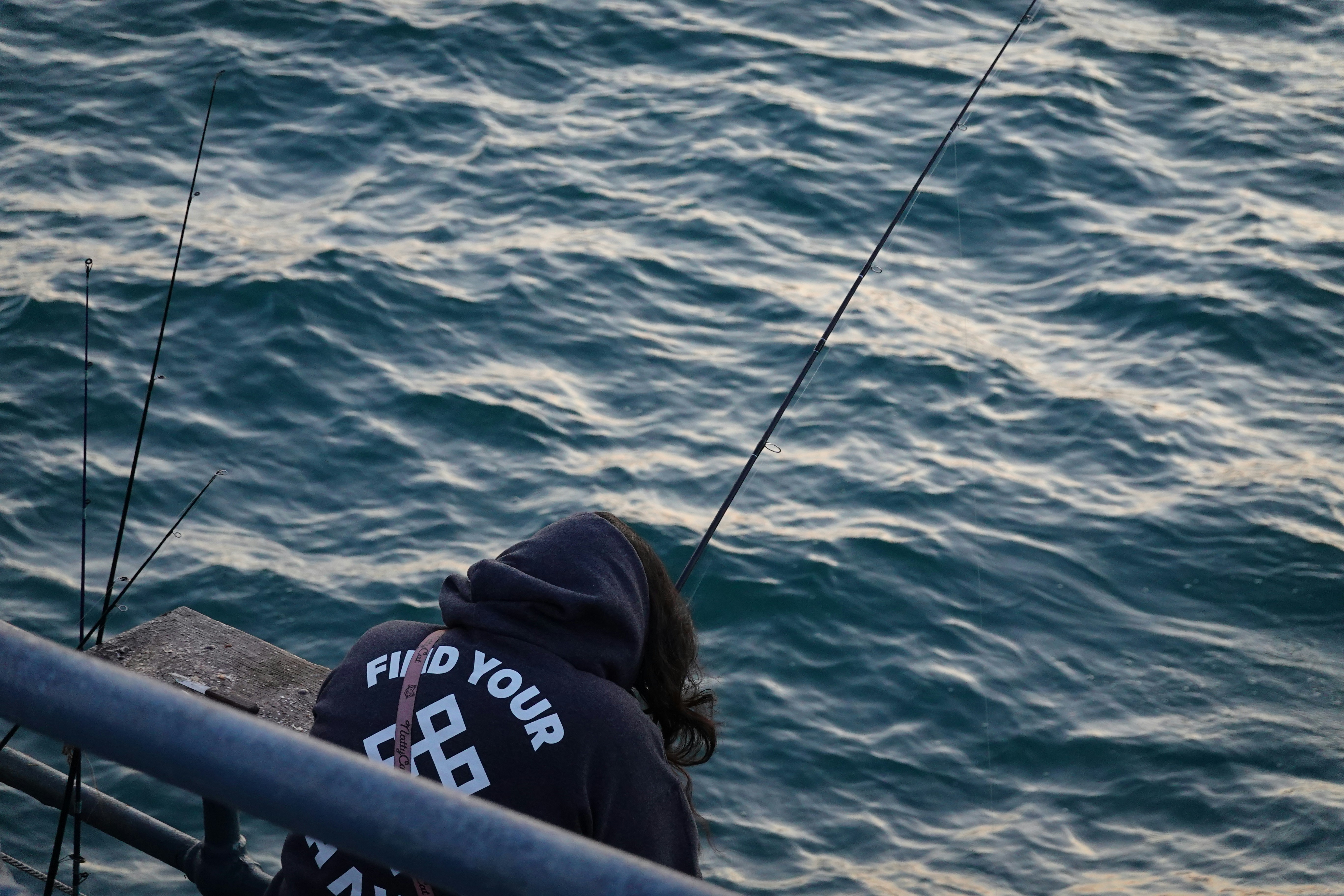 Over the Rail: A Hooded Angler Quietly Watches the Sea