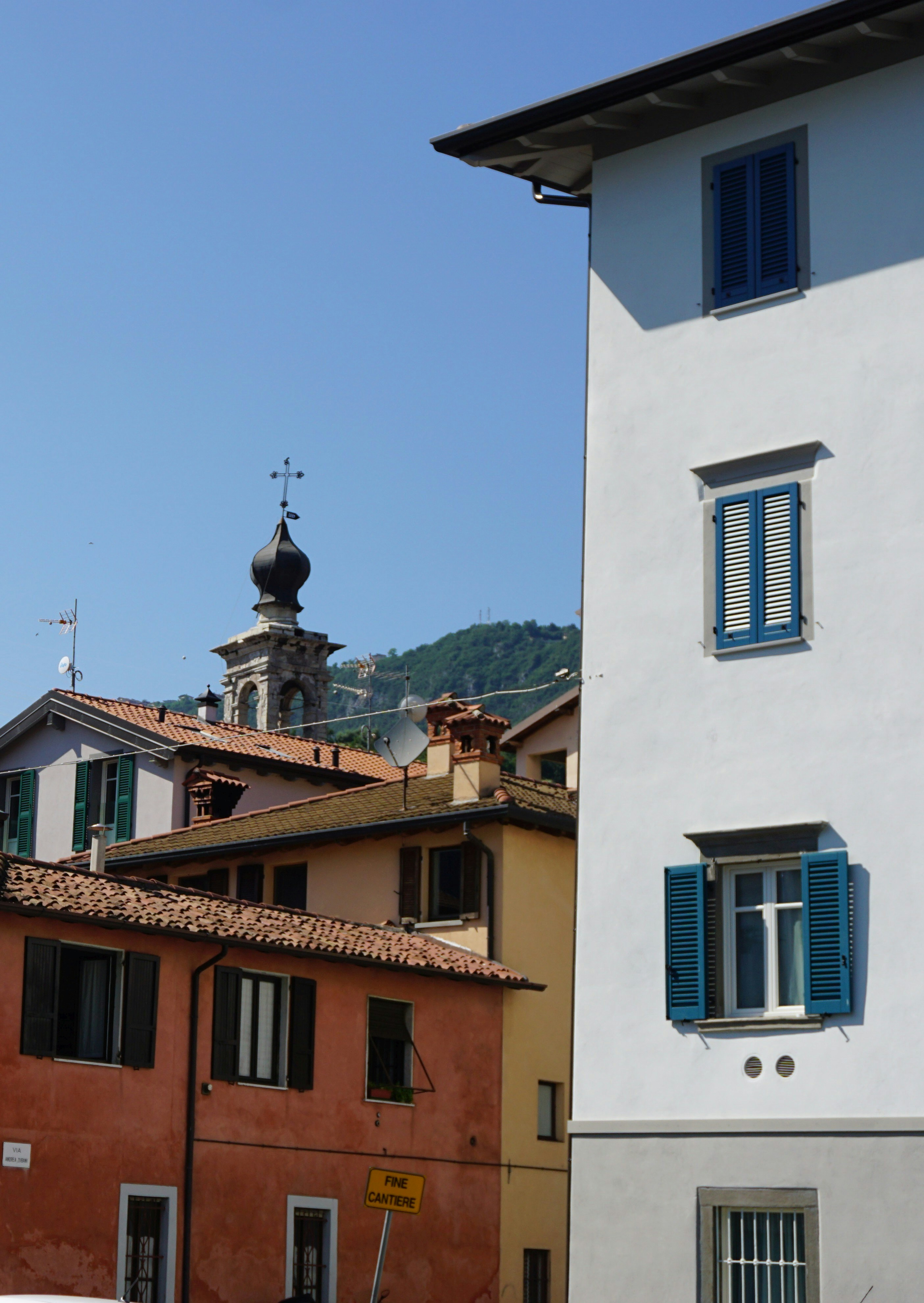 Domed Quiet on a Sunlit Street: A hillside town framed by blue shutters and terracotta roofs