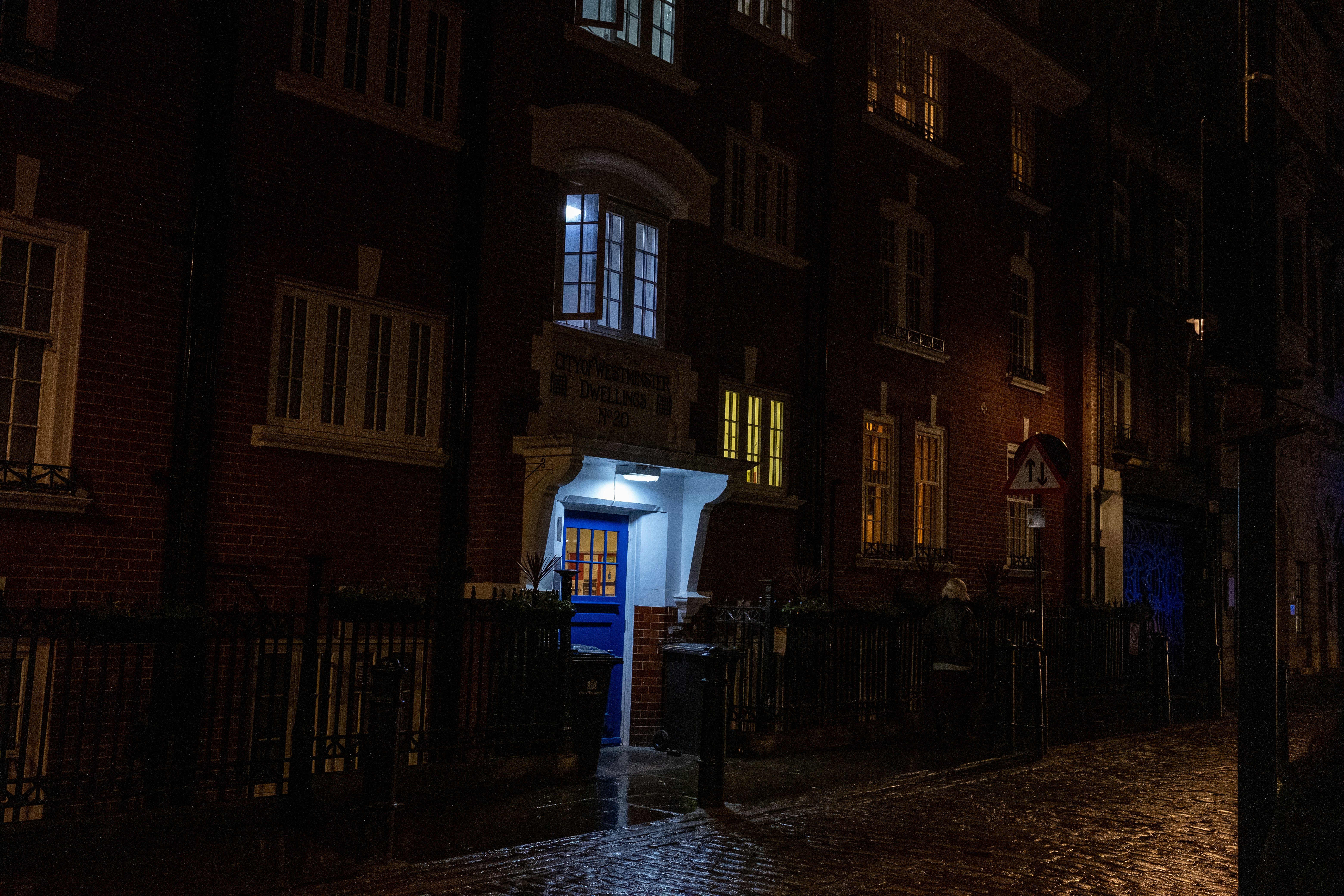 Illuminated entrance of a historic building on a rainy night, showcasing the contrast of warm light against cool shadows.
