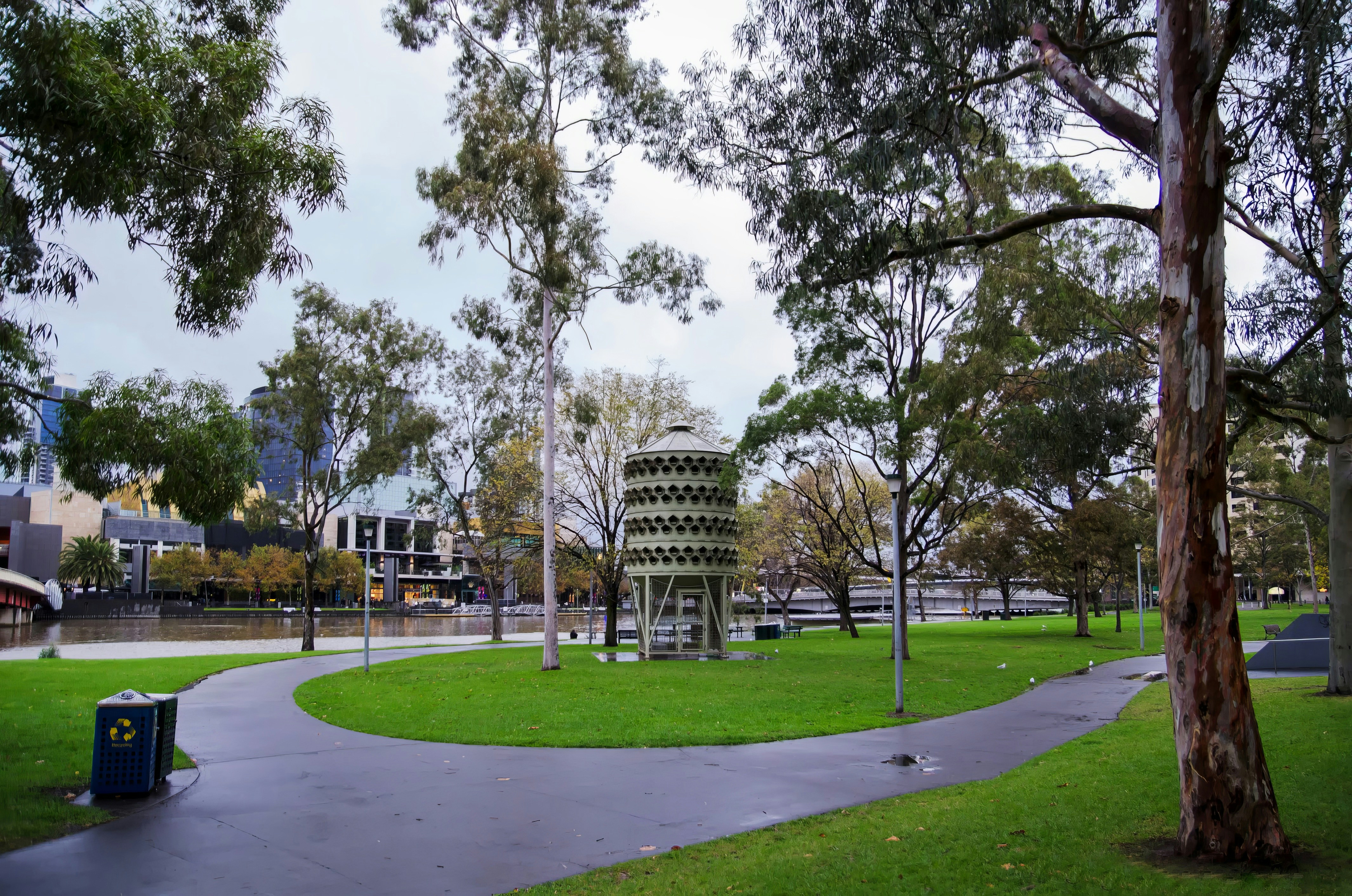Curved path through a lush park with a striped water tank and city buildings in the background.