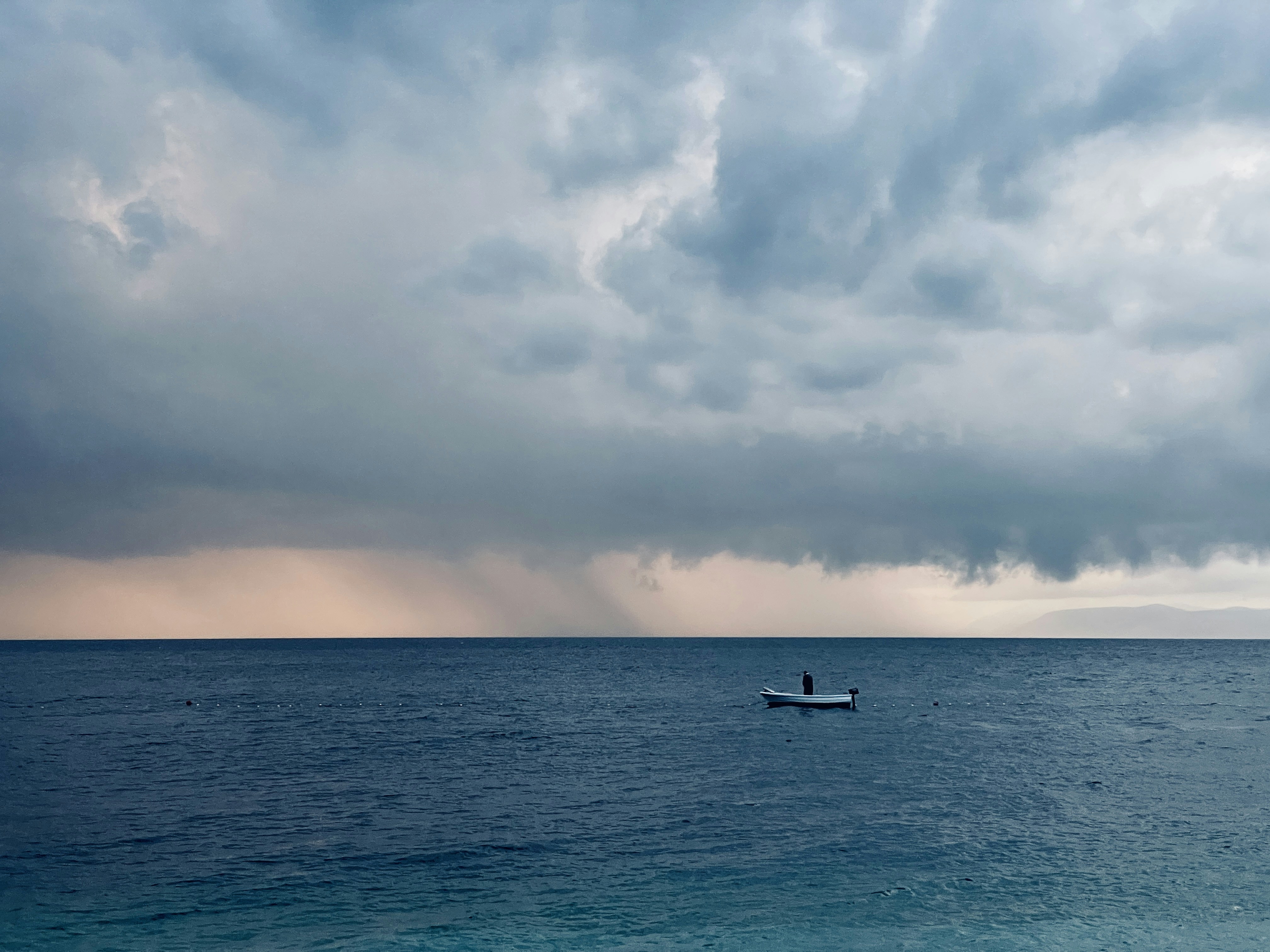A lone boat on a calm sea beneath a dramatic cloudbreak