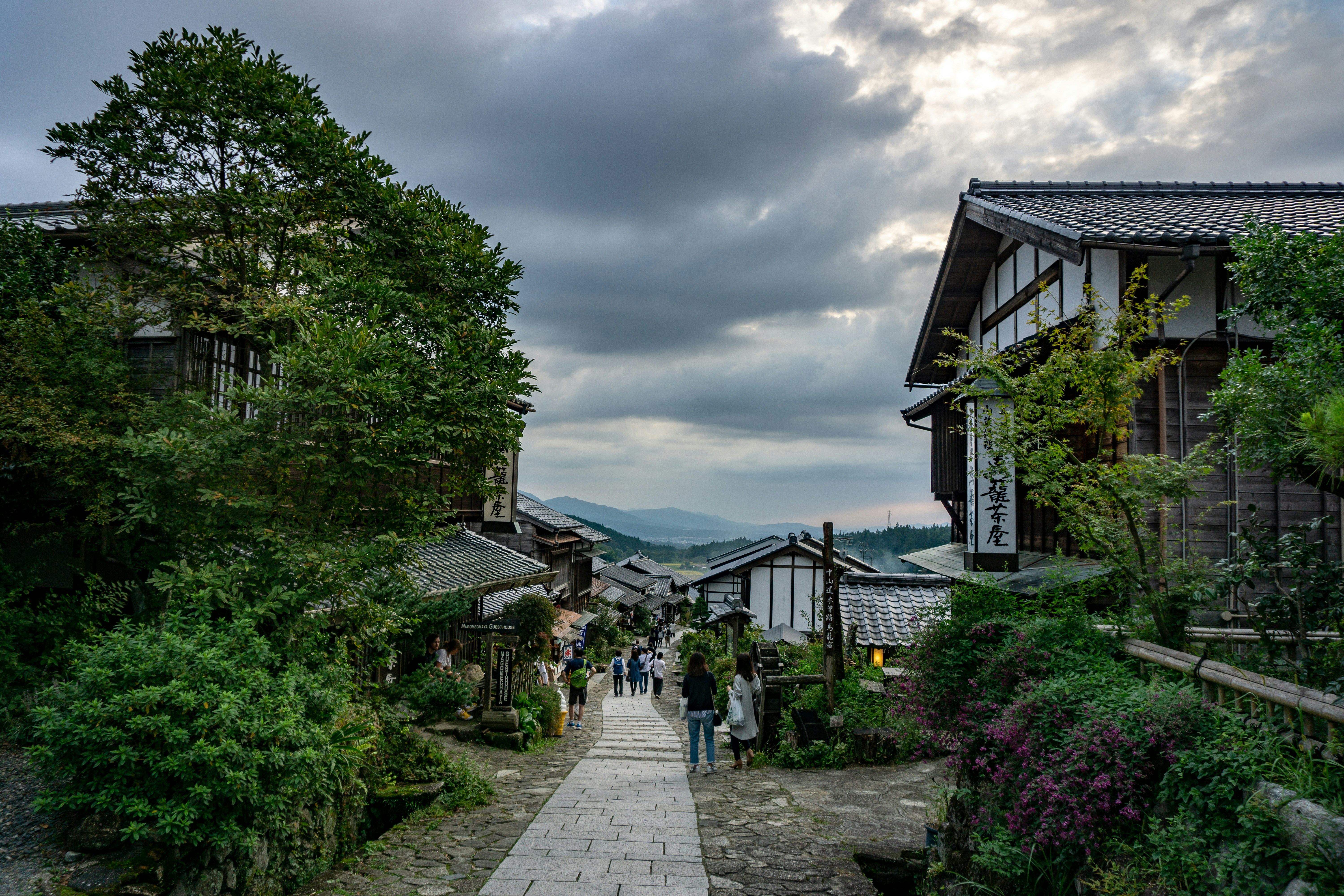 Narrow stone path flanked by traditional wooden houses under a cloudy sky.