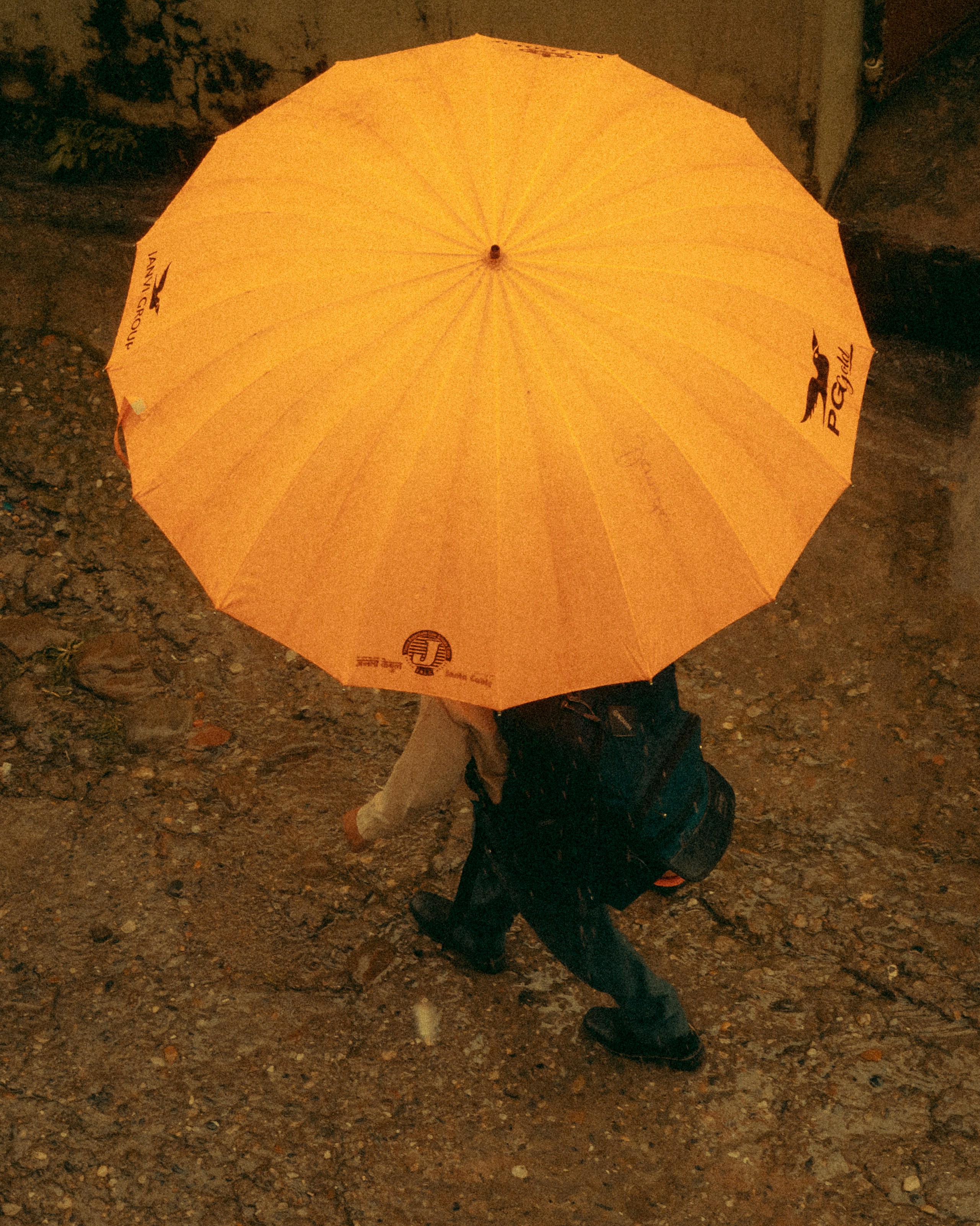 Bird's-eye view: a hiker sheltered beneath a bright orange umbrella on a rocky path