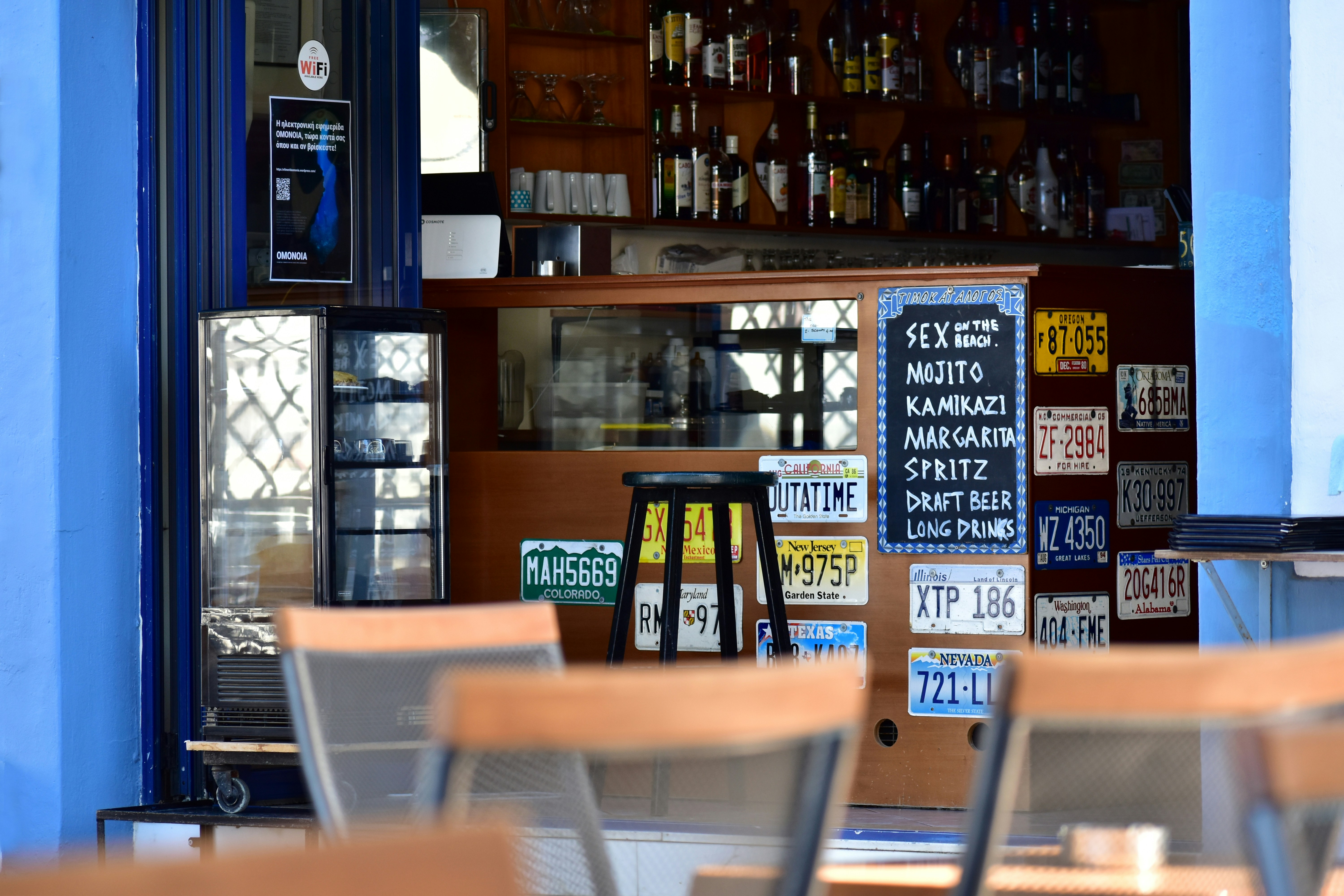 A cozy bar scene featuring a wooden stool and a vibrant display of drink specials on colorful license plates. The inviting atmosphere hints at a lively social space.