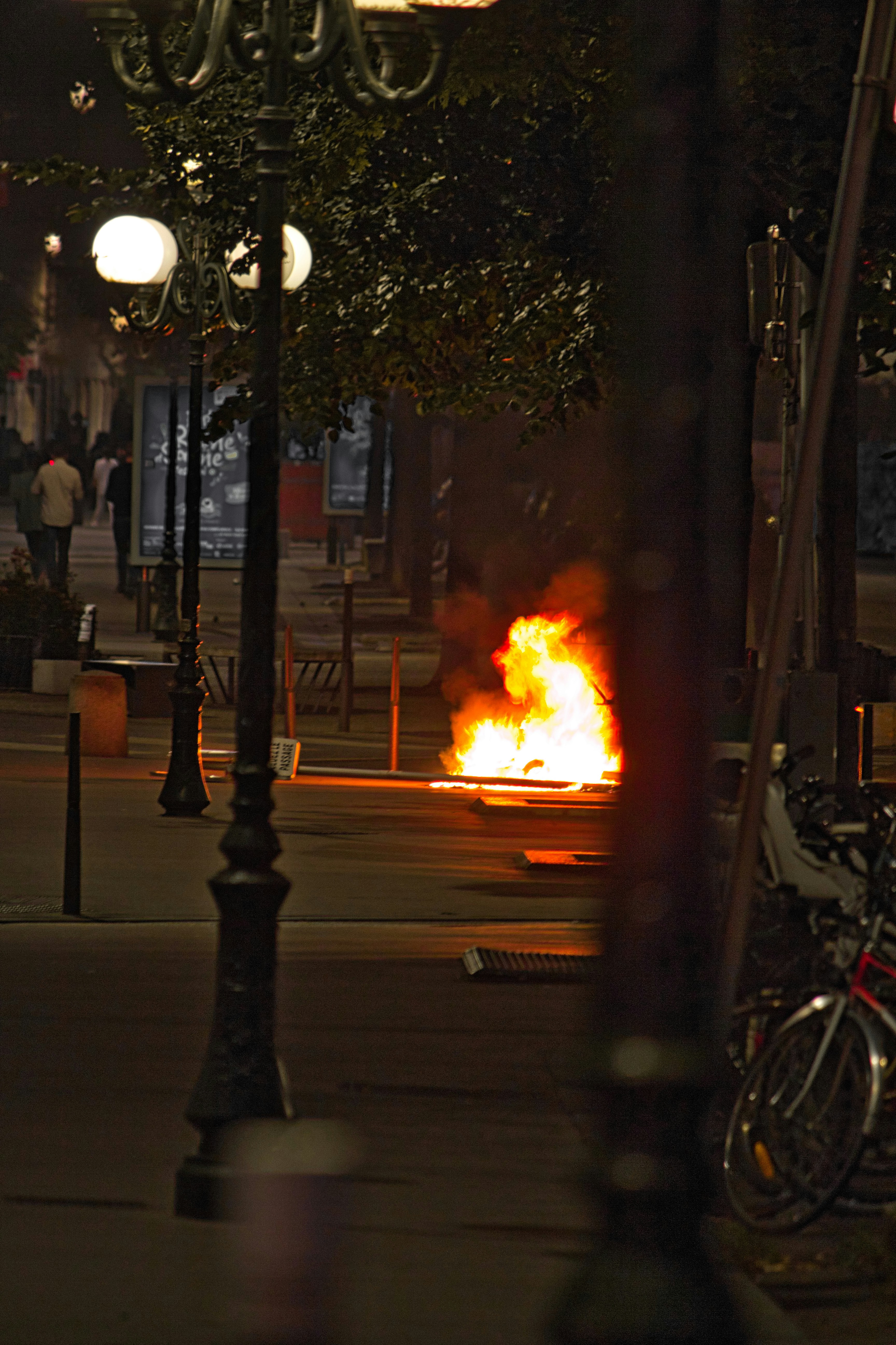 City Street Blaze: Firelight Between Lamps and Bikes