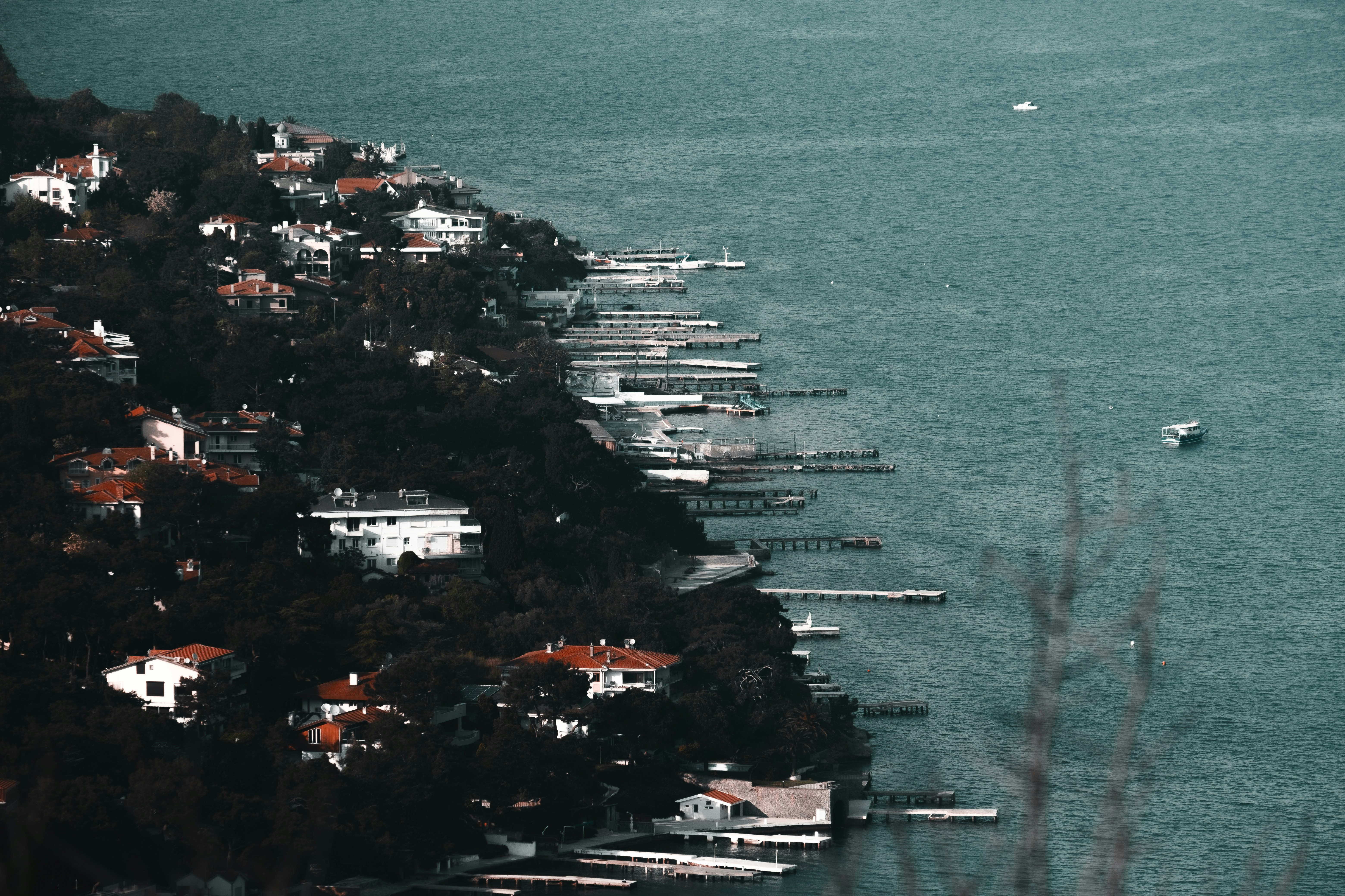 Hillside village with red-roofed homes and a row of wooden piers along teal water