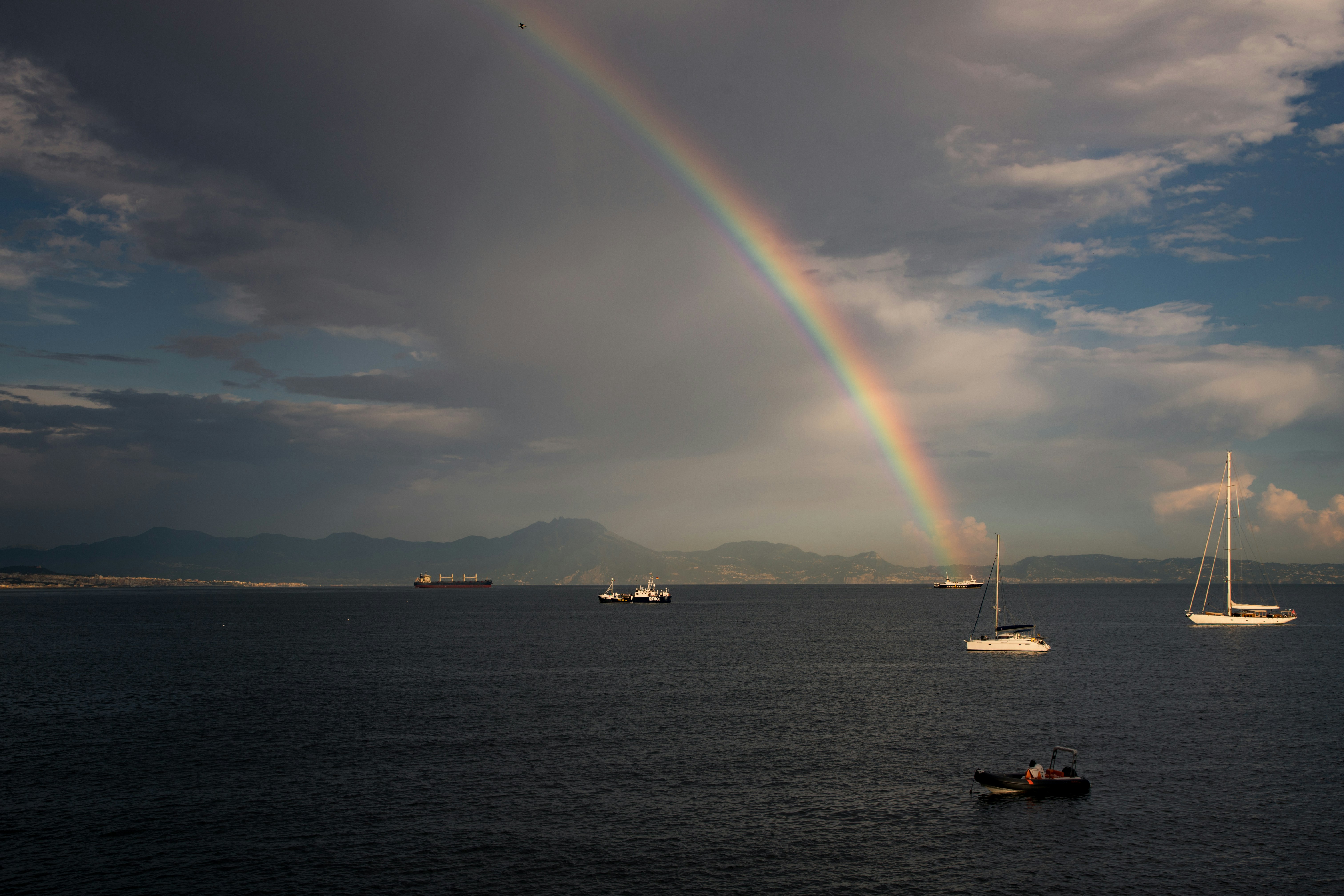 Rainbow Over a Quiet Harbor: Sailboats, Mist, and Distant Peaks