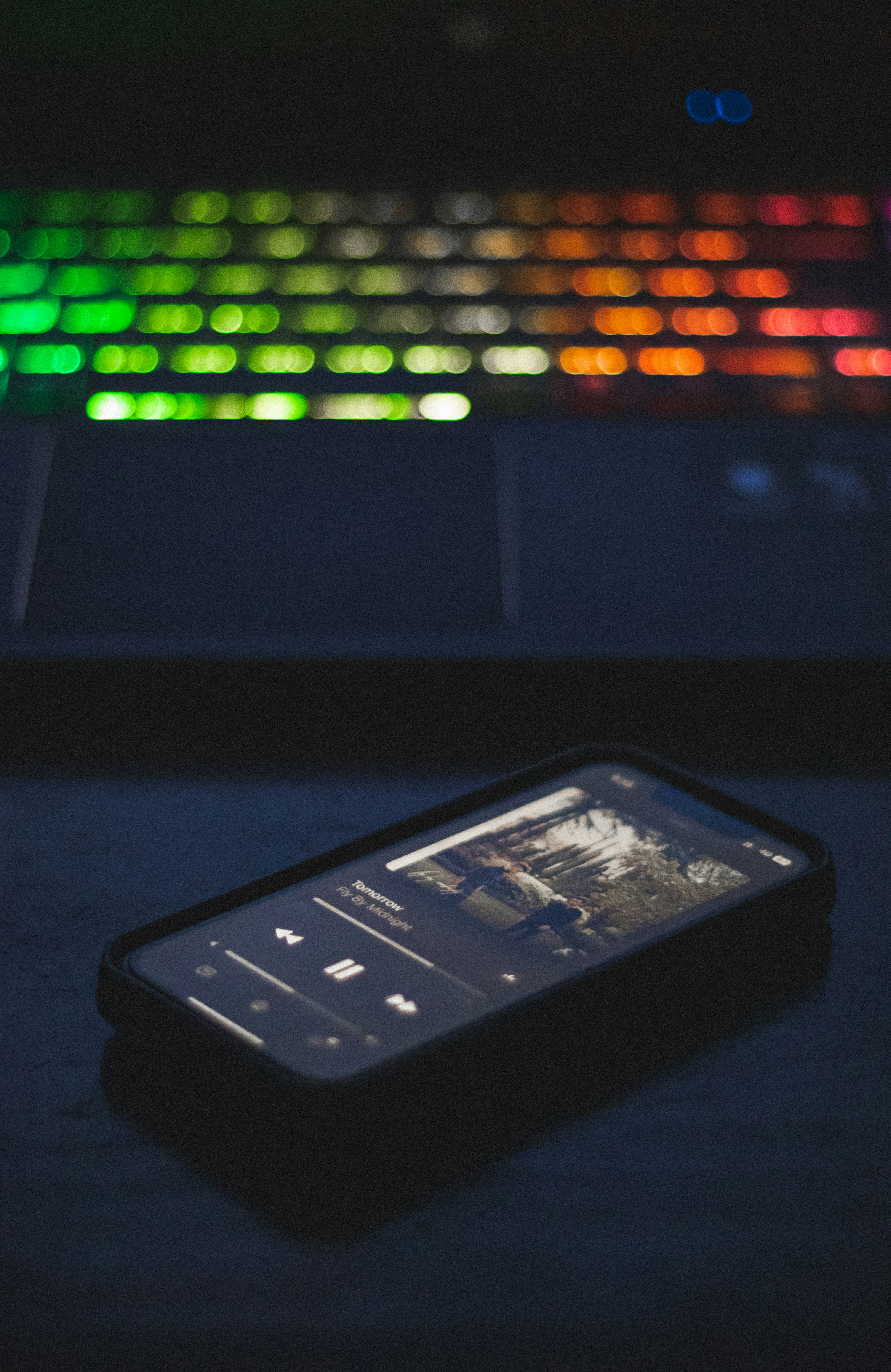 Smartphone displaying a music playlist, illuminated by the colorful glow of a nearby keyboard.