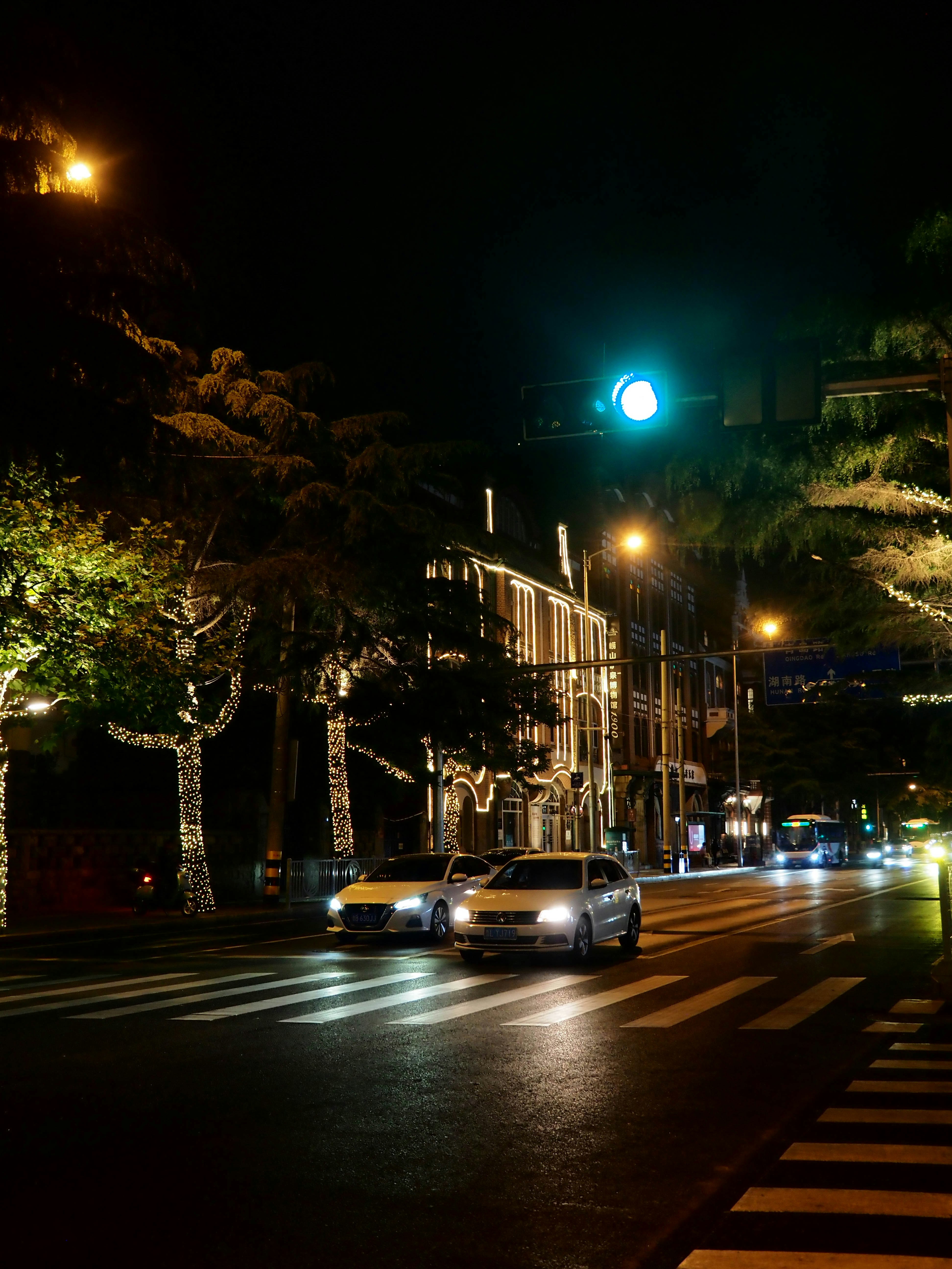 Blue Signal Over a Neon-Lit Street: Nighttime City Scene with Crossing Cars