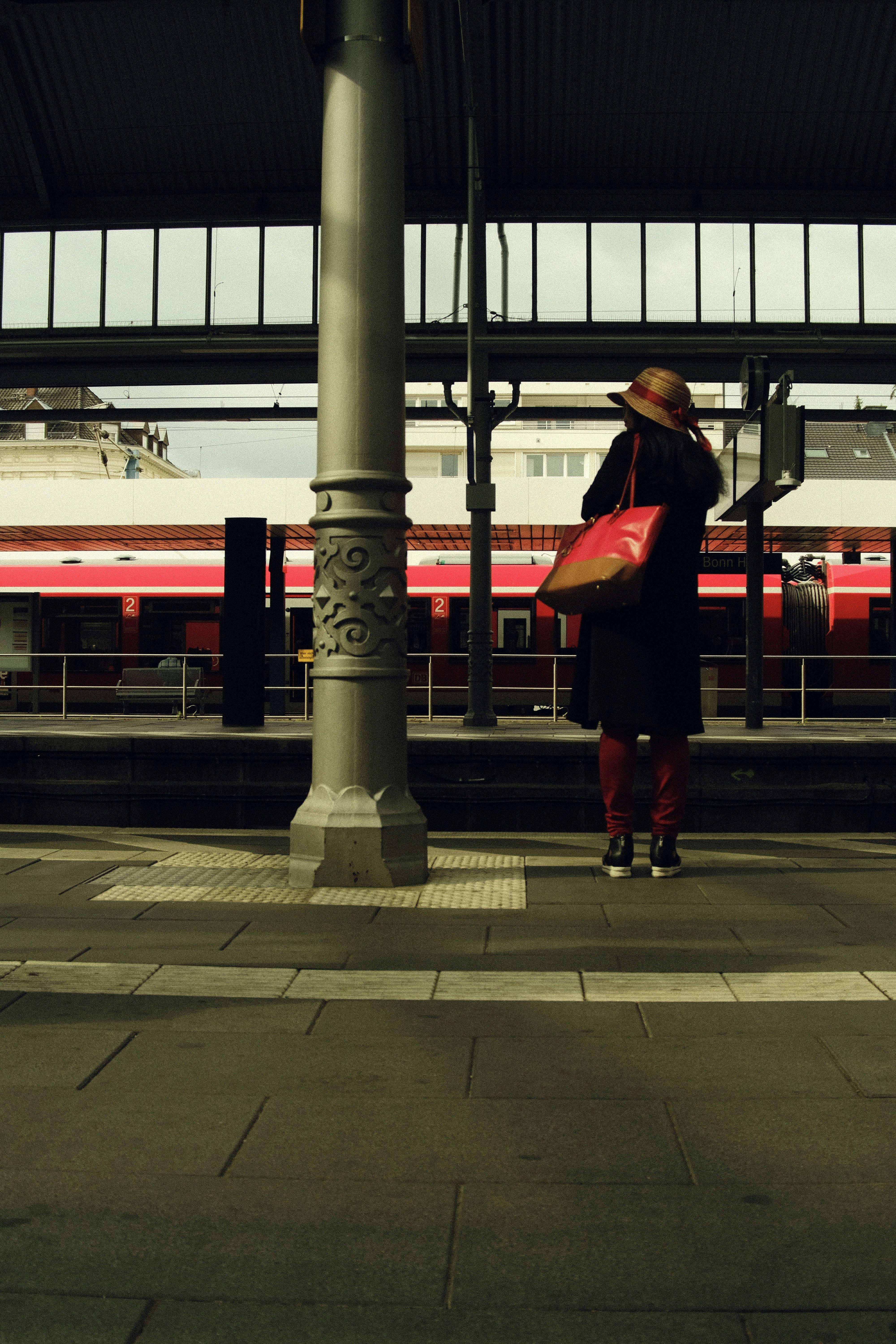 I call this one "The lady in red". It was a spontaneous shot at a train station. The column and its shadow along the grey foreground, next to the stinging red clothes of the lady, which compliments the reds of the train in the background. In my opinion one of my best shots