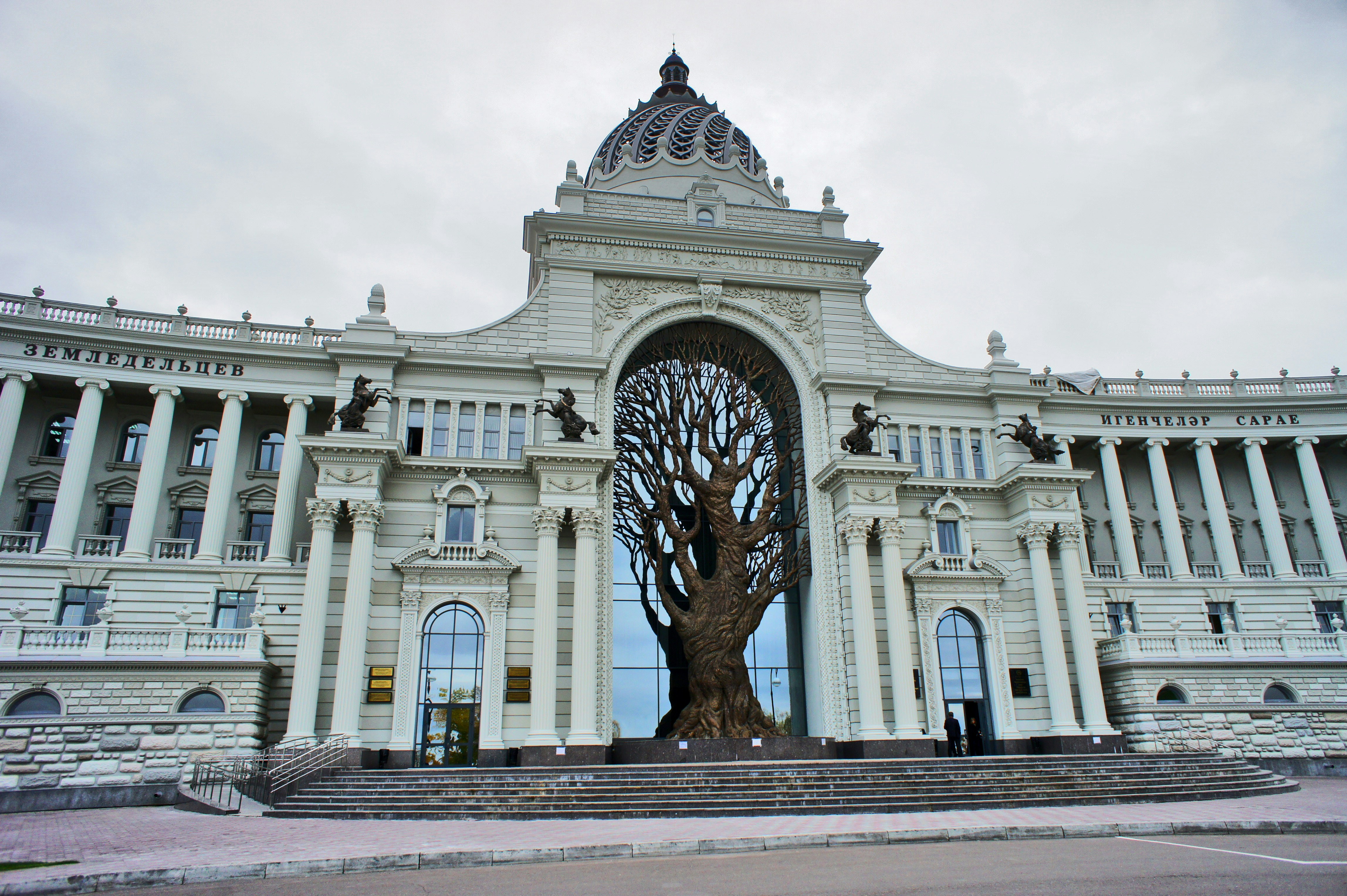 Grand neoclassical building with a central arch and a large tree sculpture in Kazan.
