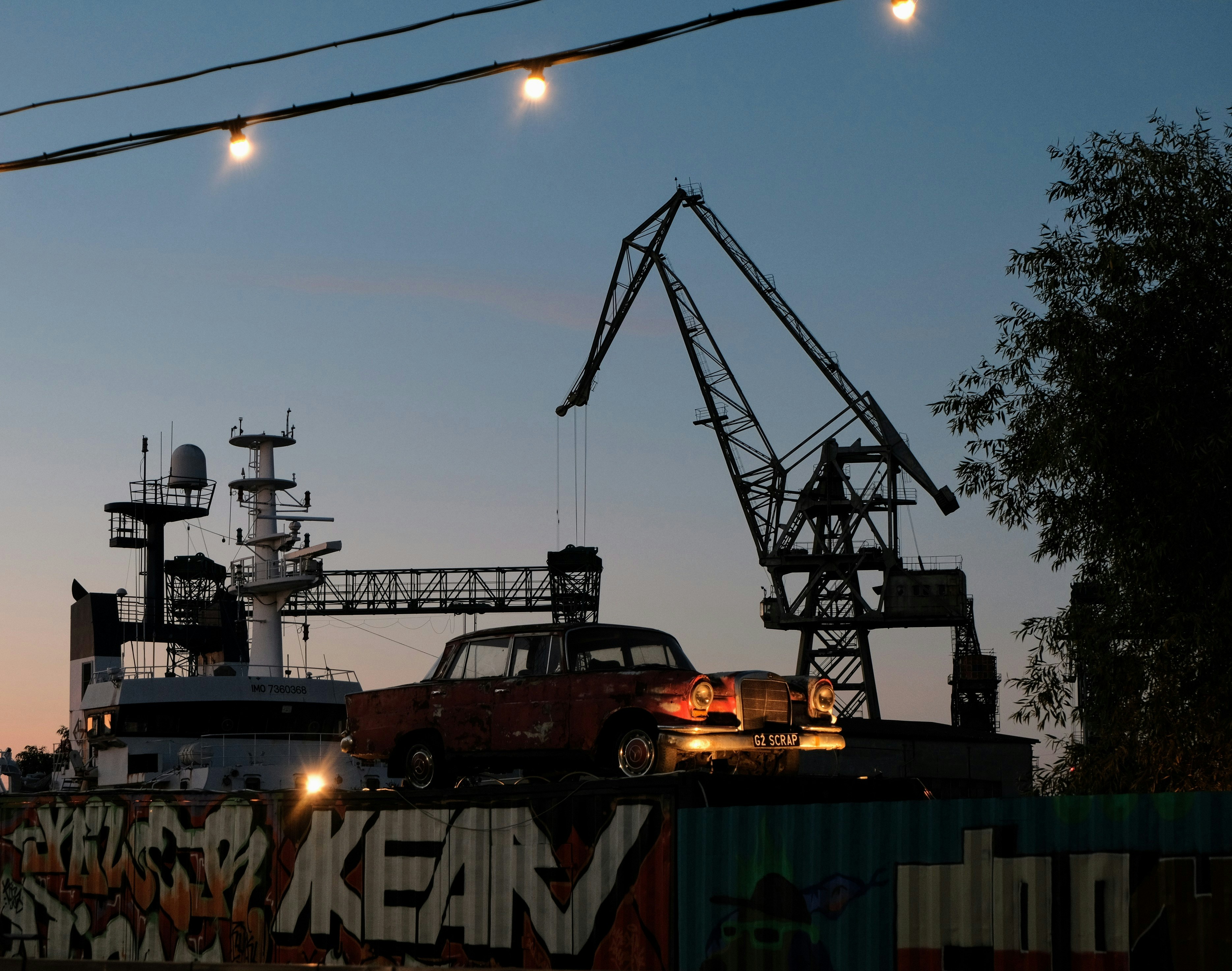 Rusted Car on a Crane-Lit Dock at Twilight
