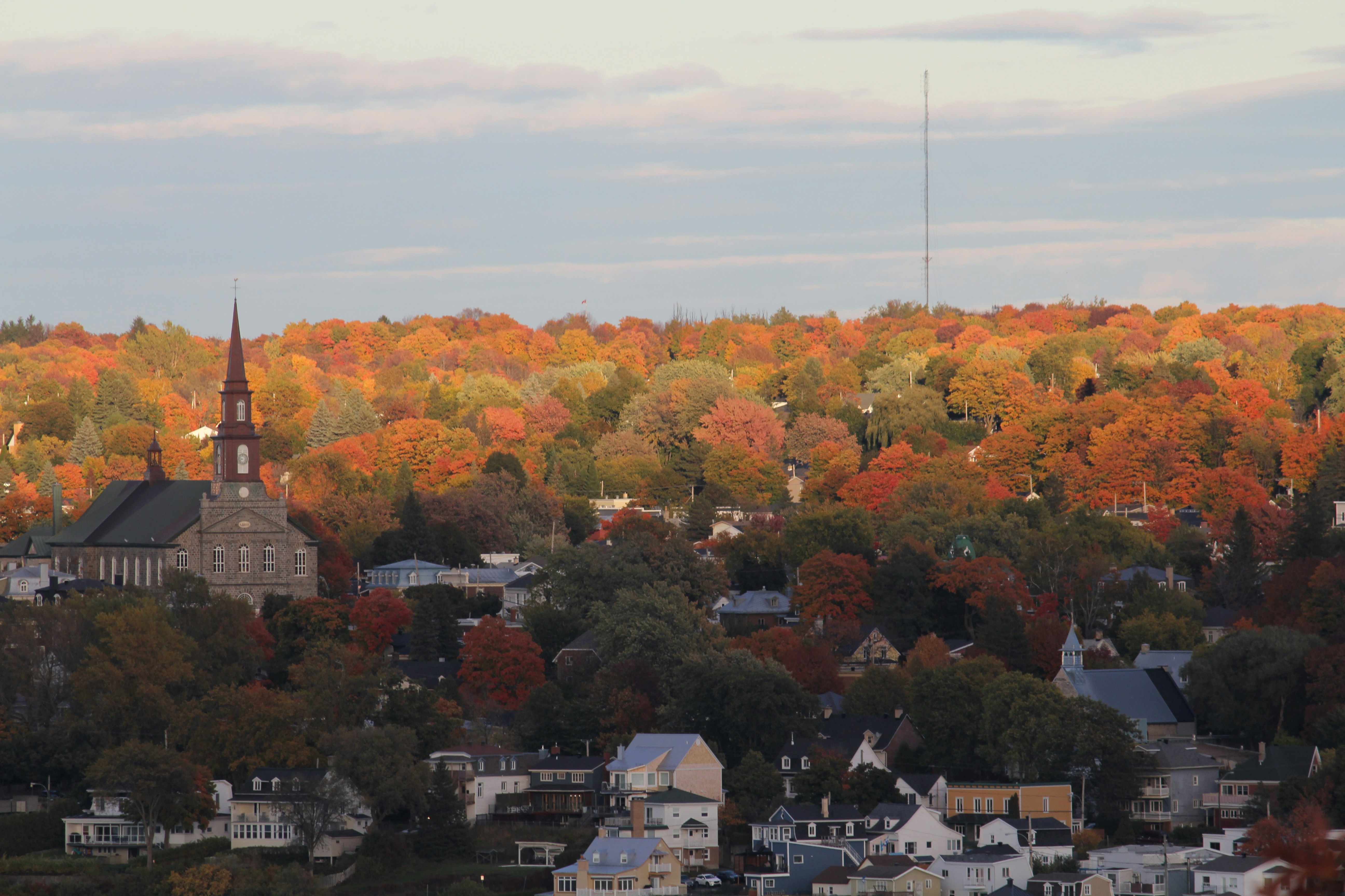 Church spire rising above a town, surrounded by vibrant autumn foliage under a partially cloudy sky.