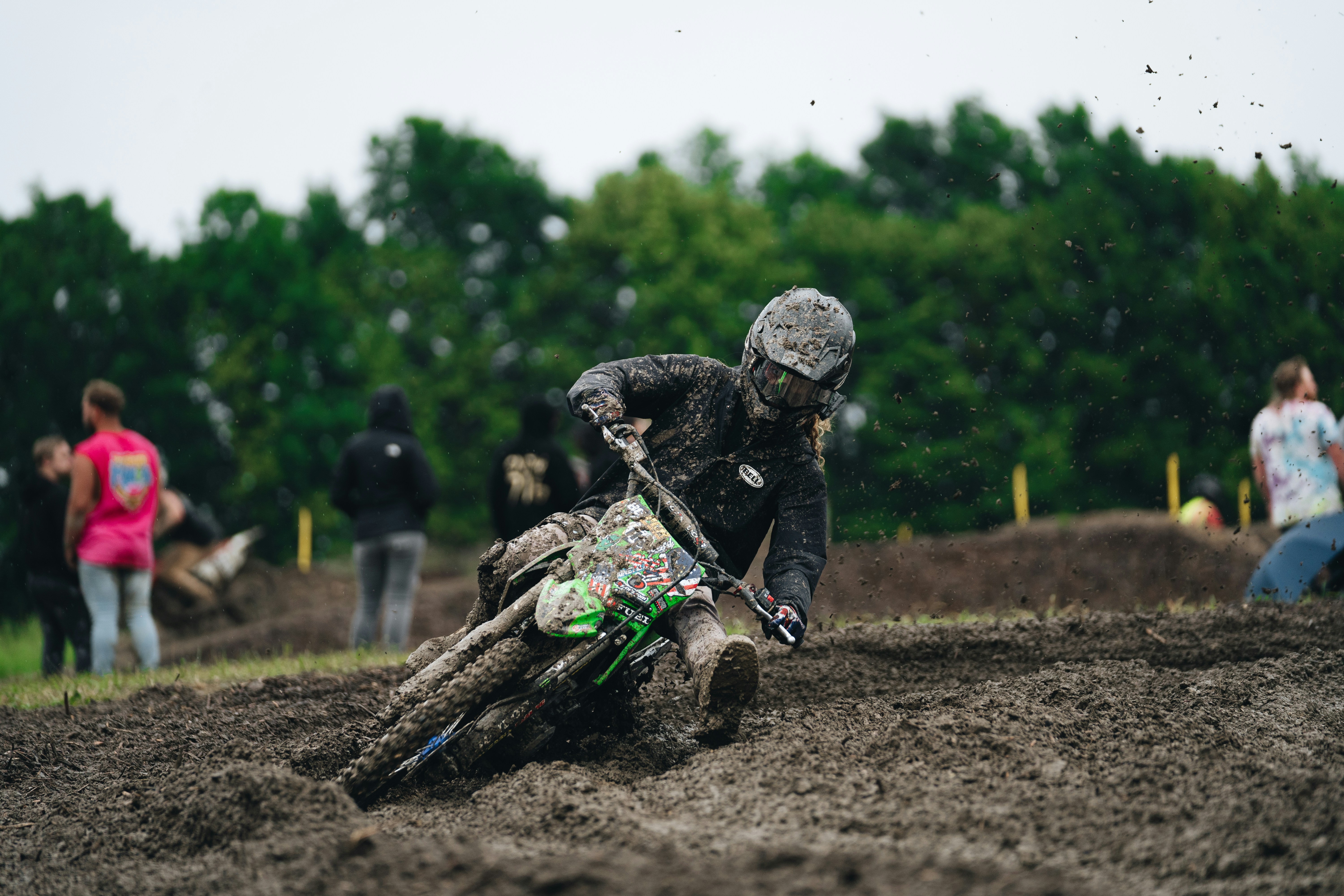 Dirt bike rider navigating a muddy track with spectators in the background.