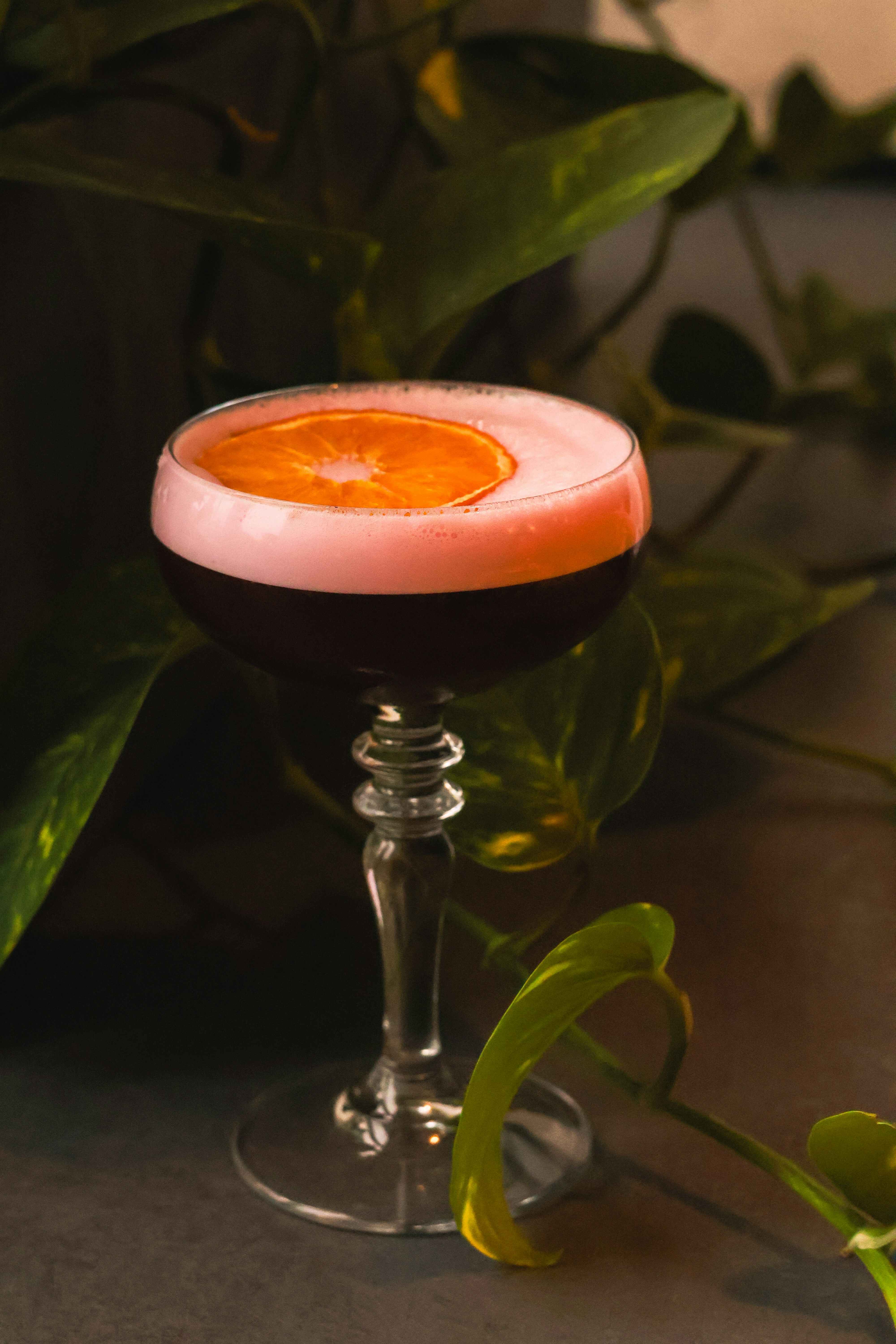 Amber Cocktail on a Glass Stem Against Verdant Backdrop