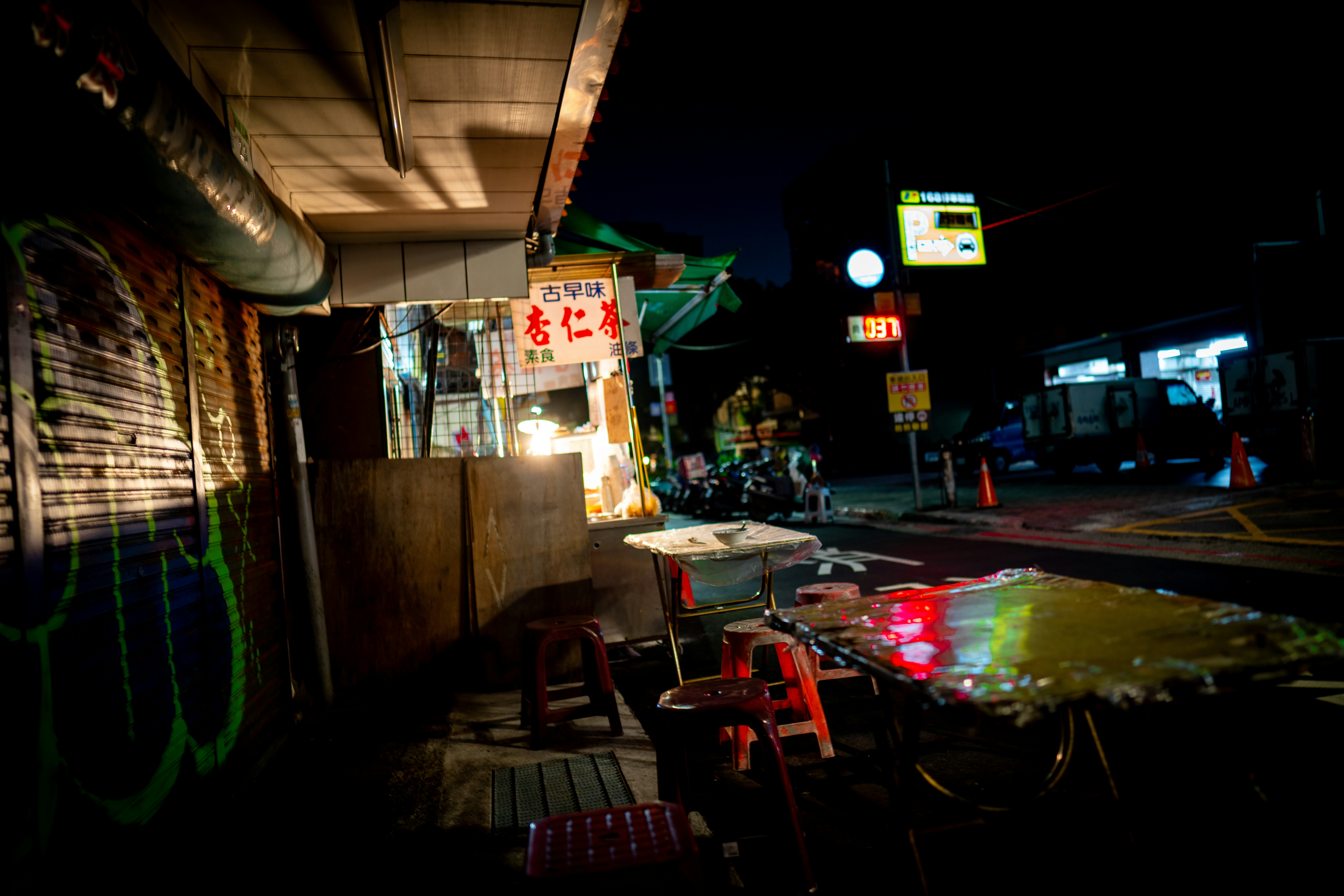 Dimly lit street food stall with empty tables reflecting neon lights, creating an inviting yet tranquil atmosphere.