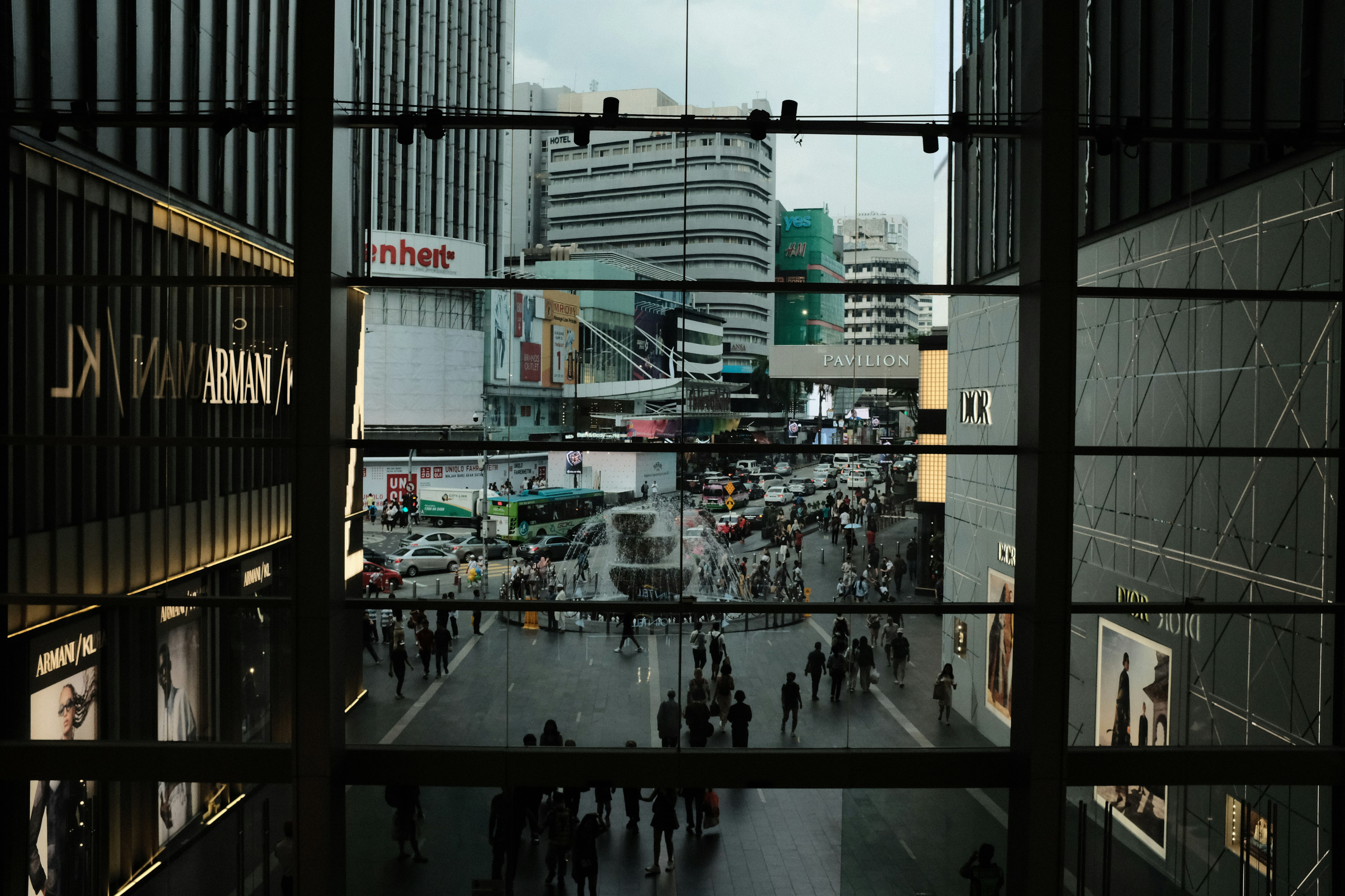 View through glass panels of a bustling city intersection with high-rise buildings and busy streets.