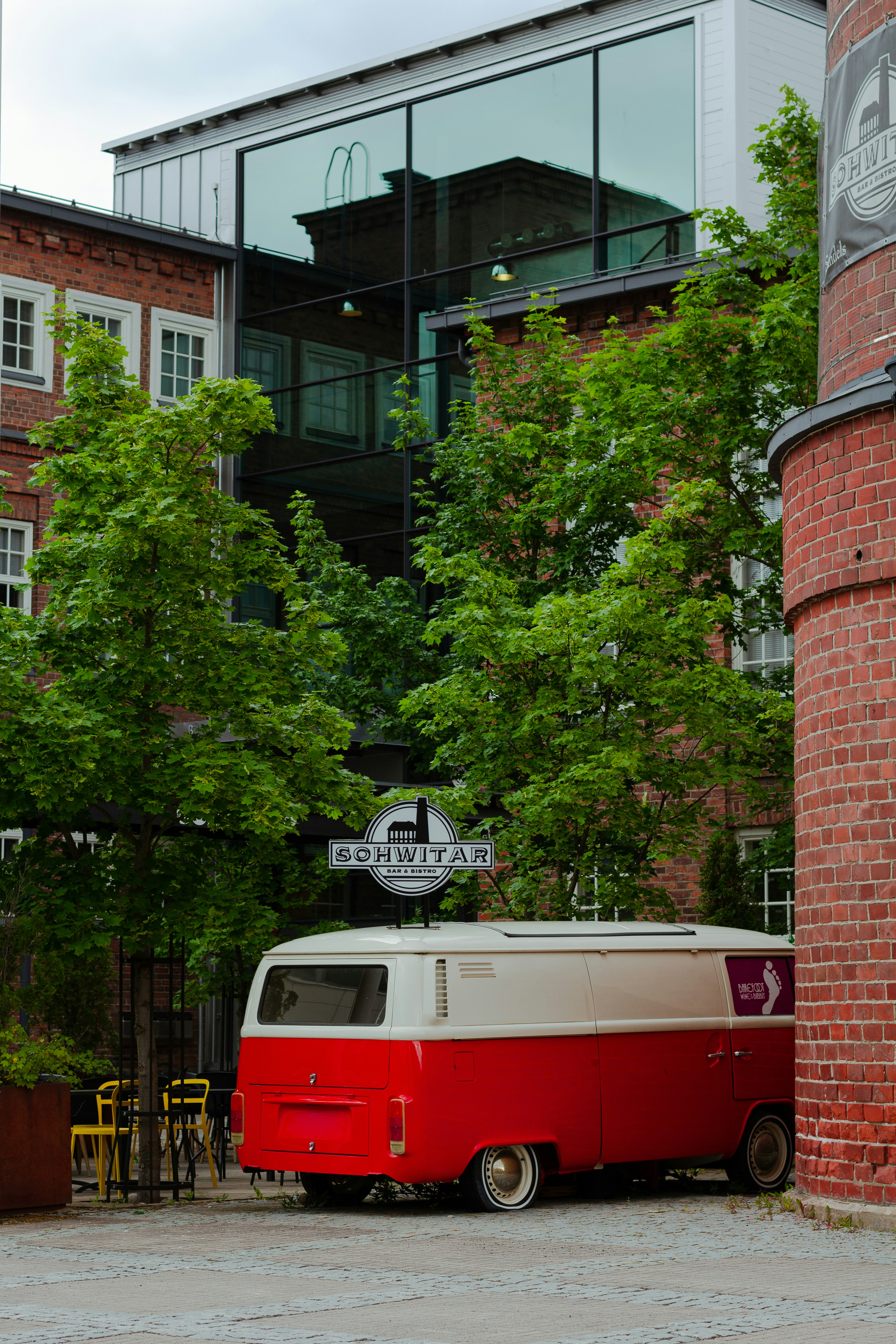 Red VW Camper Anchored Between Brick and Glass in a Quiet Urban Scene