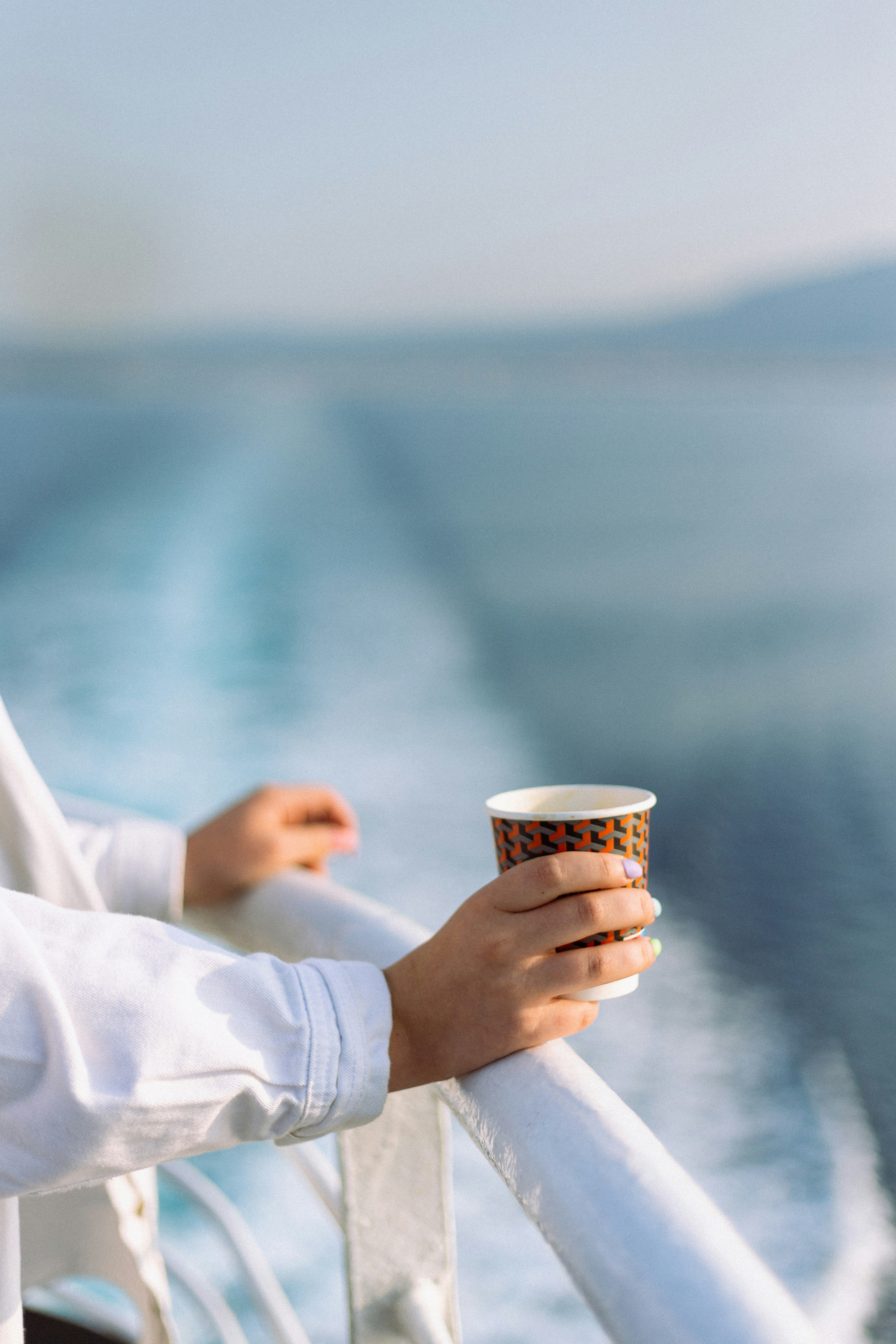A Quiet Moment on the Rail: Cup in Hand Against Open Water