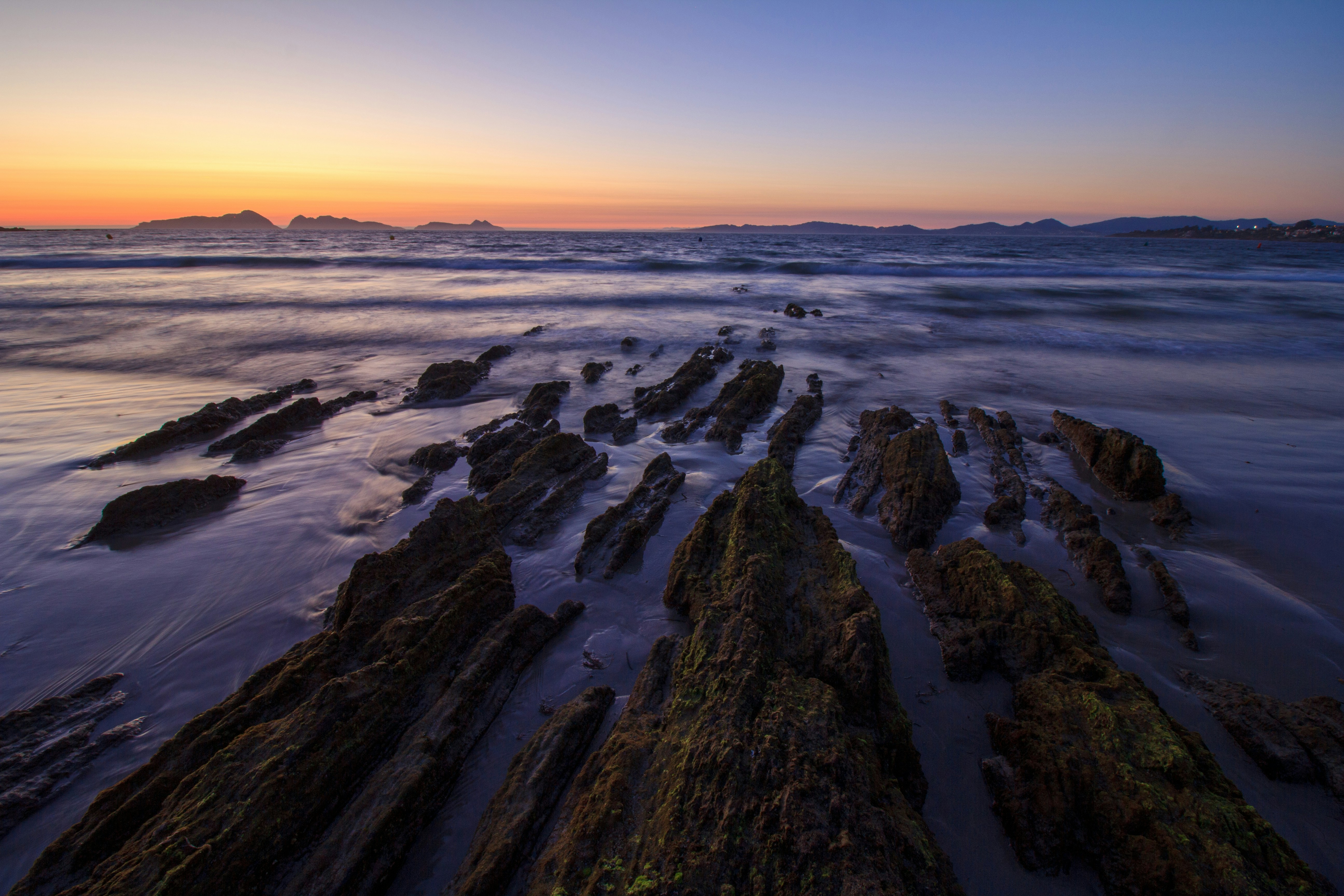 Rock formations lead into the ocean under a colorful sunrise sky.