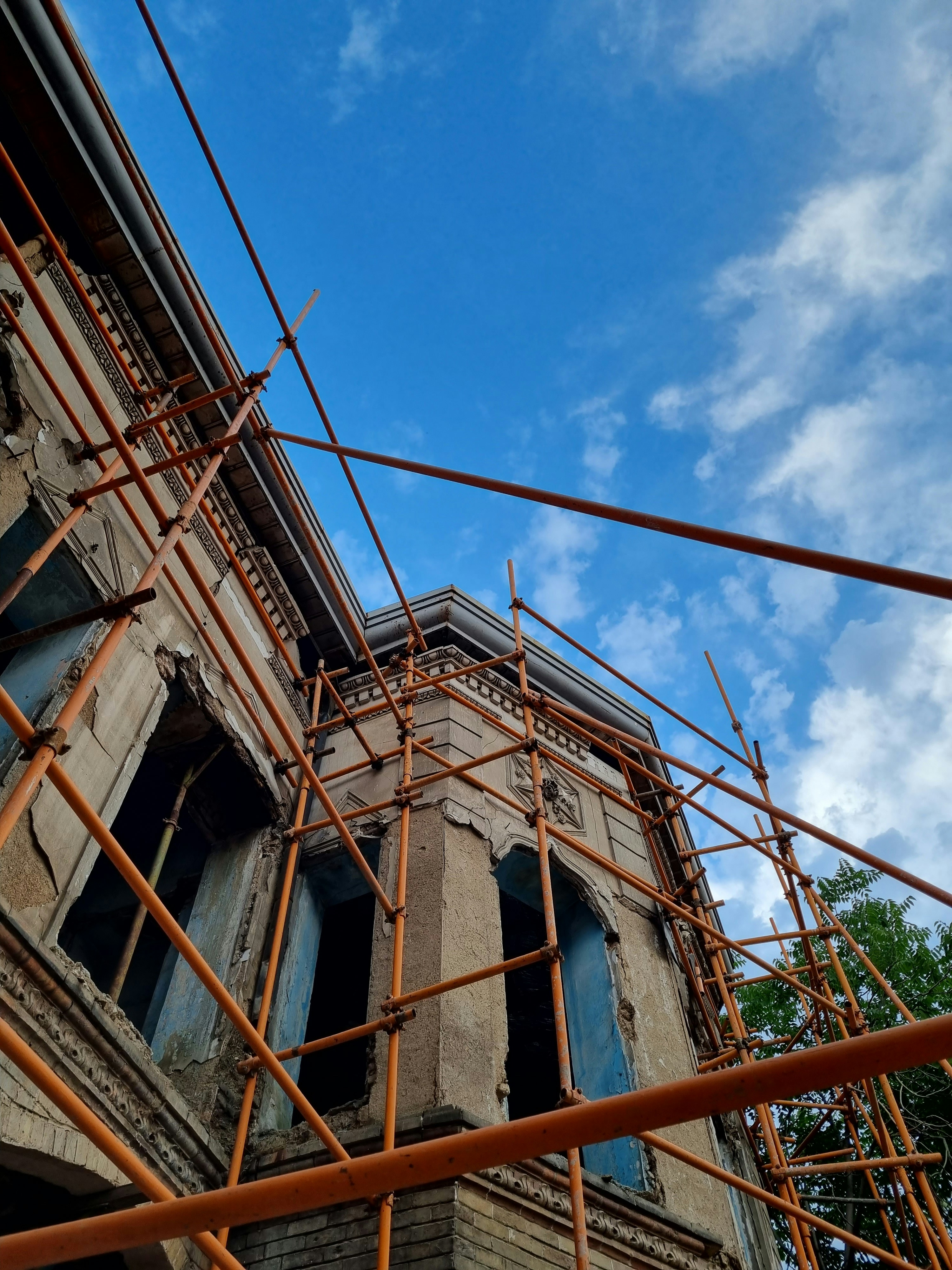 Rising Frame: Scaffolding Embraces a Weathered Facade Under a Clear Blue Sky