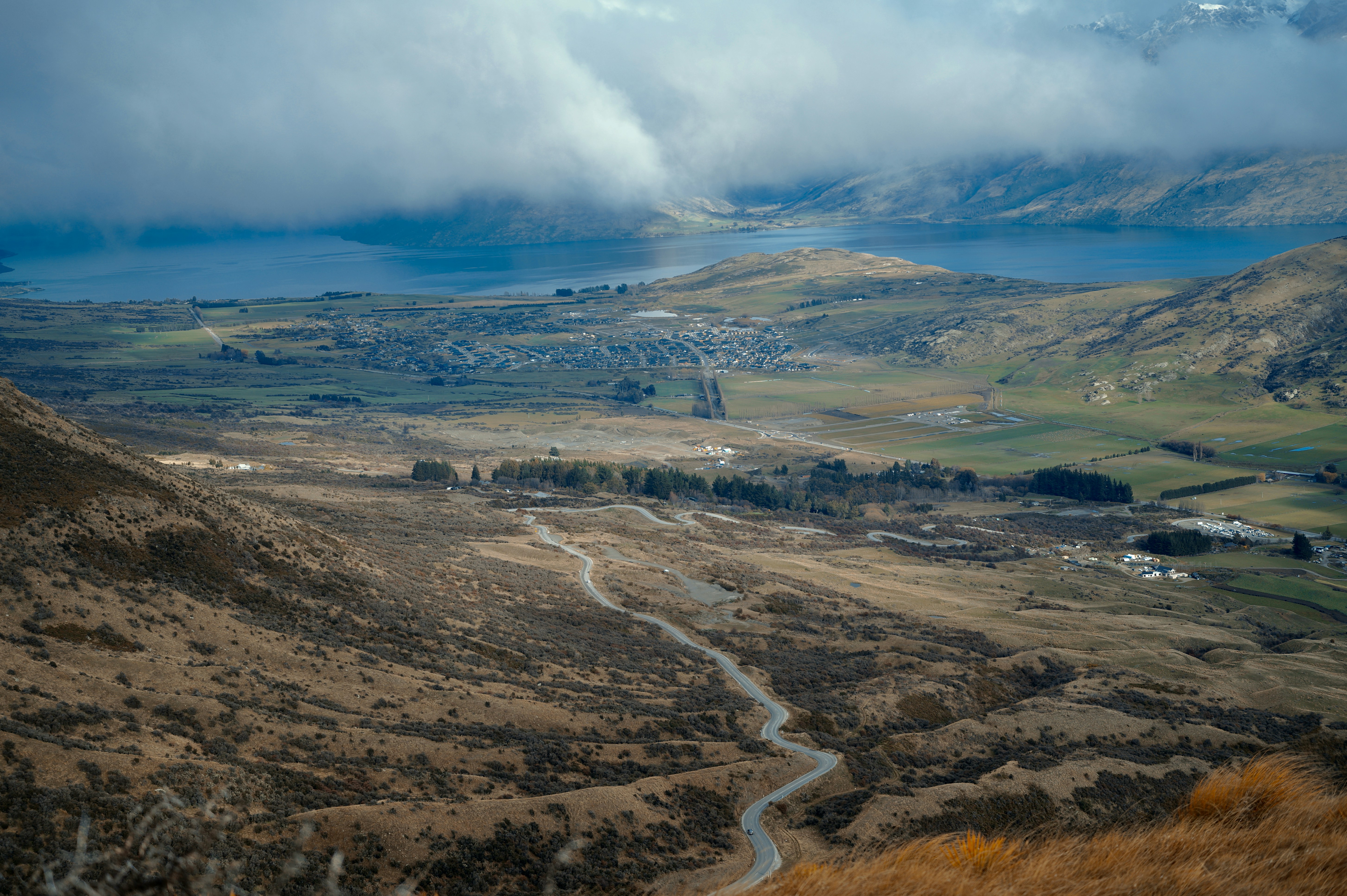 Winding Path Toward a Lakeside Hamlet Beneath Looming Clouds