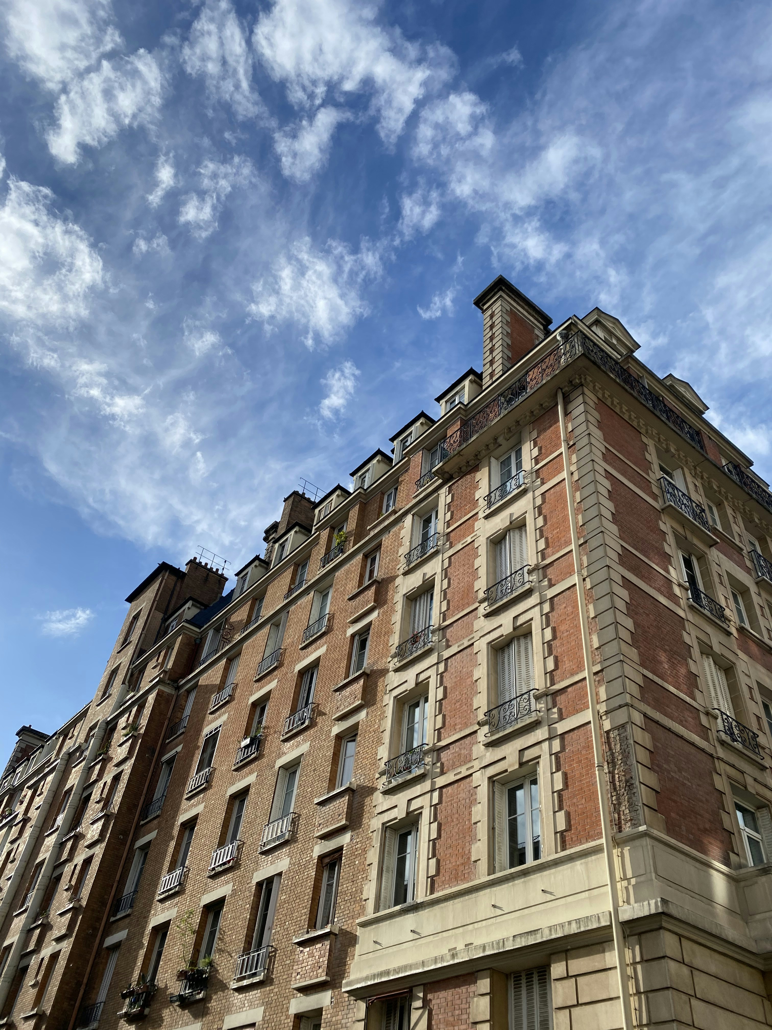Historic brick building with intricate details against a backdrop of wispy clouds in a blue sky.